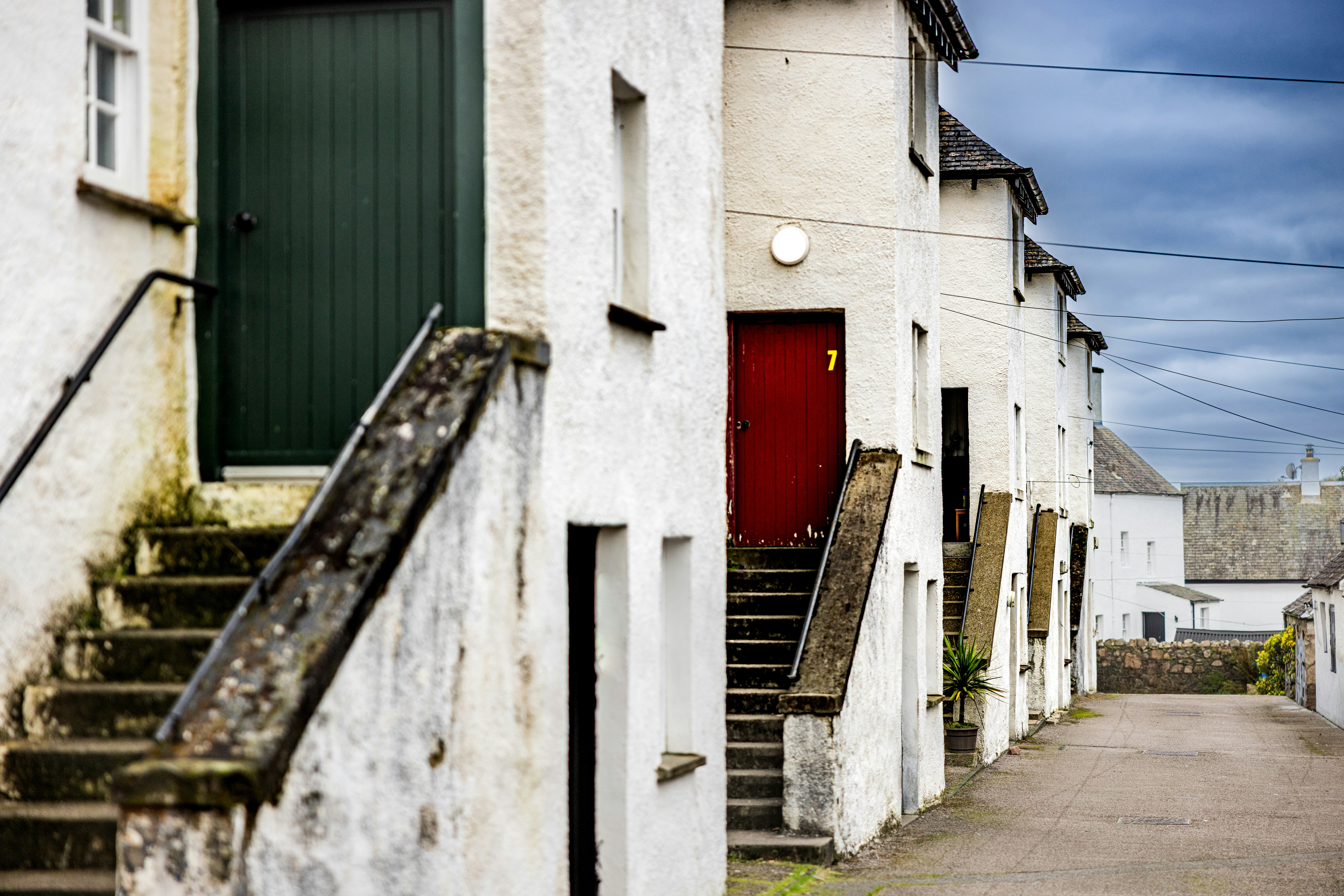 Terraced whitewashed cottages with a red door along a quiet coastal lane