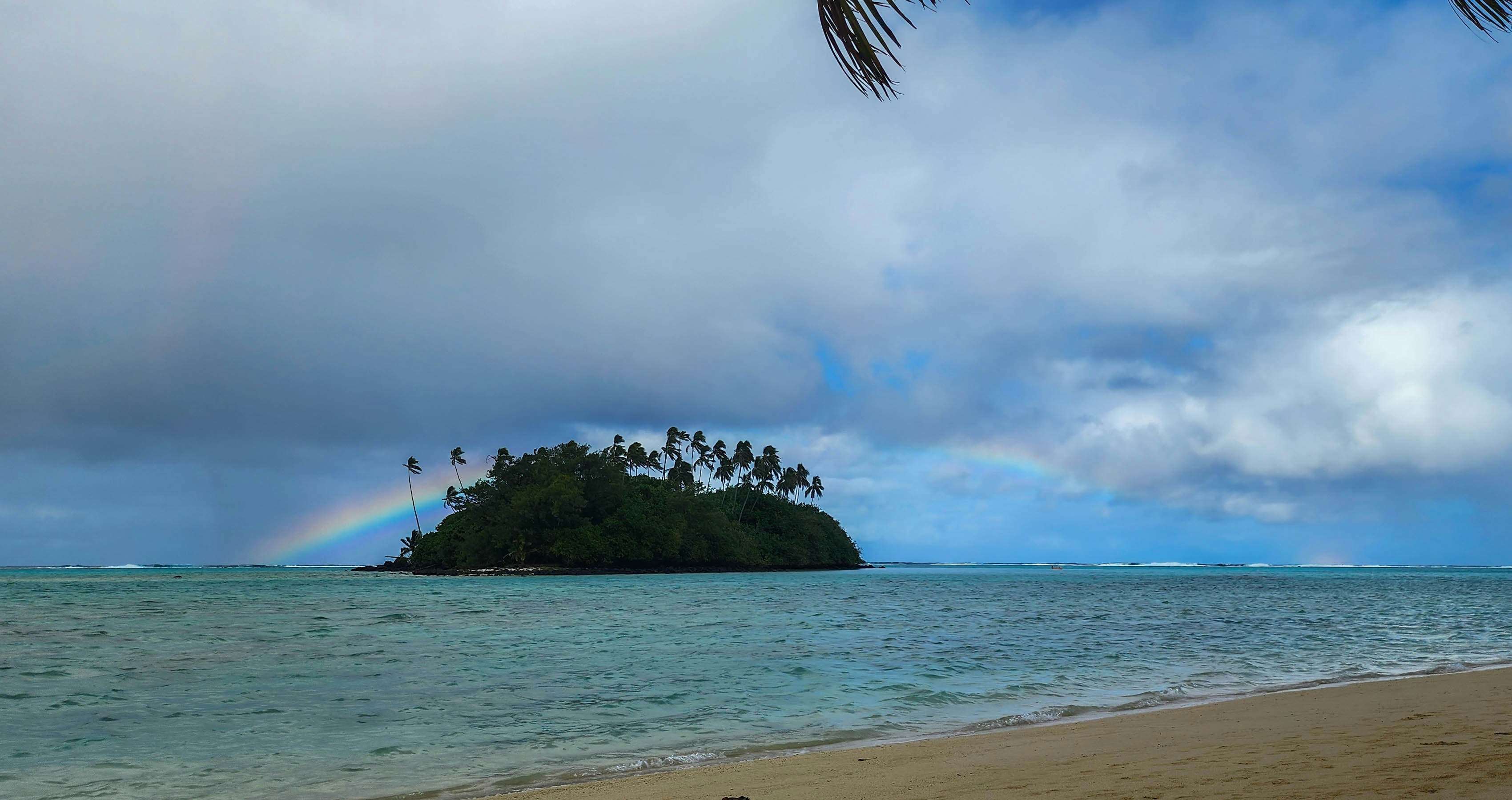 Rainbow over a small palm-dotted island framing a tranquil tropical shoreline
