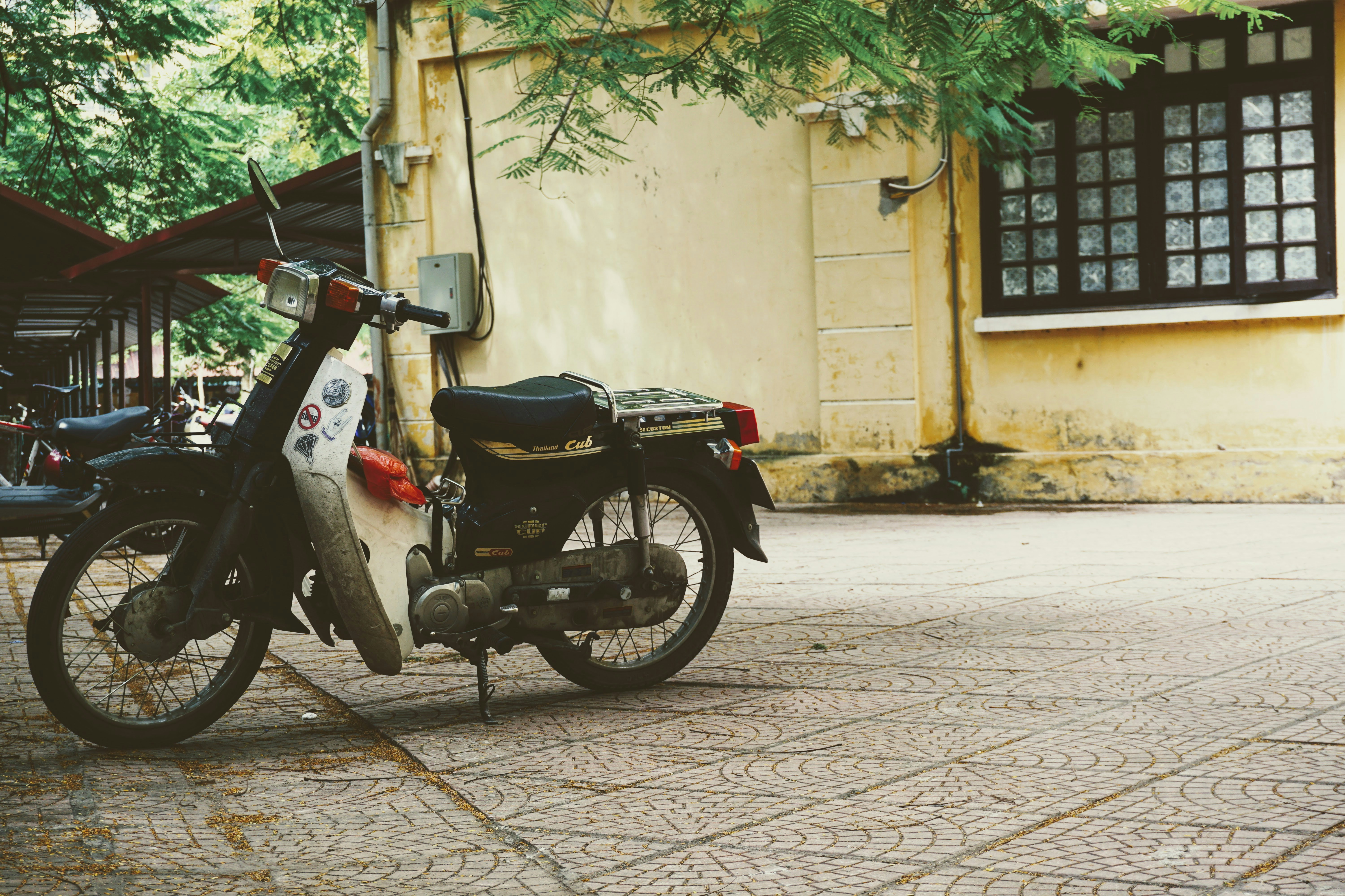 Silent Street Warrior: A Dated Scooter Resting by a Sunlit Courtyard