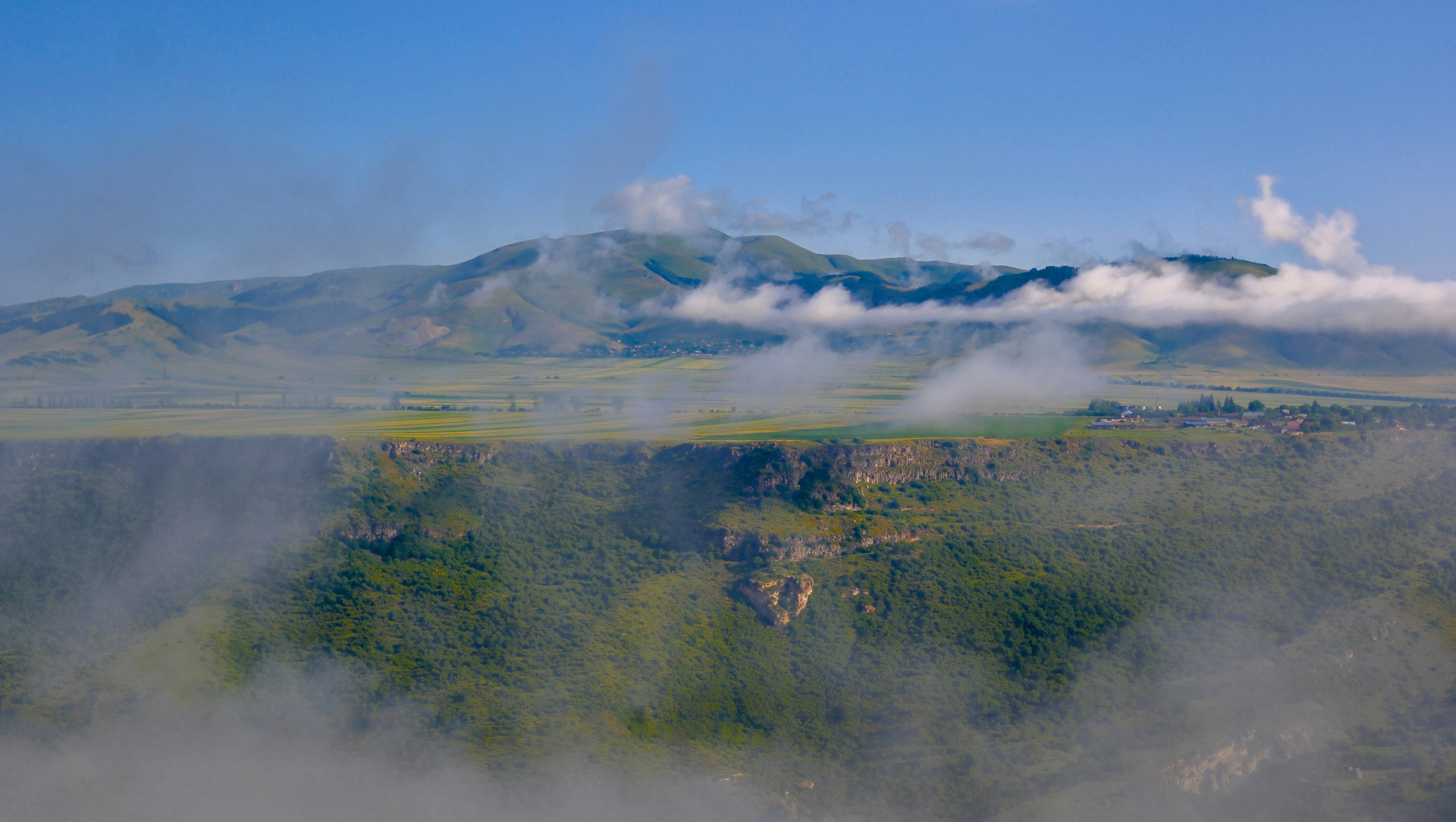 Soft morning fog lifts over a valley with a distant ridge and scattered clouds gliding above green fields.