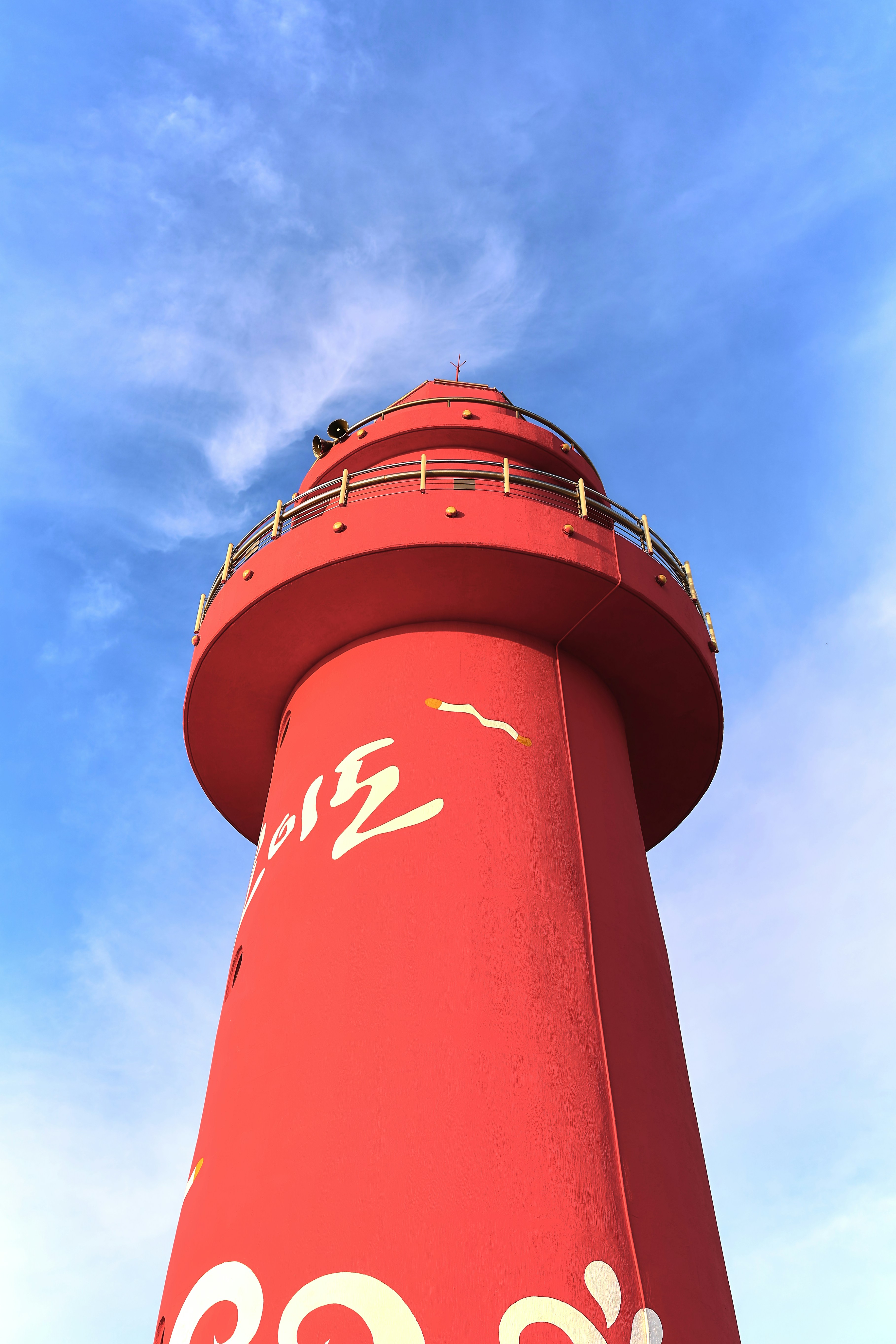 Red beacon rising: a low-angle portrait of a striped lighthouse against a clear blue sky