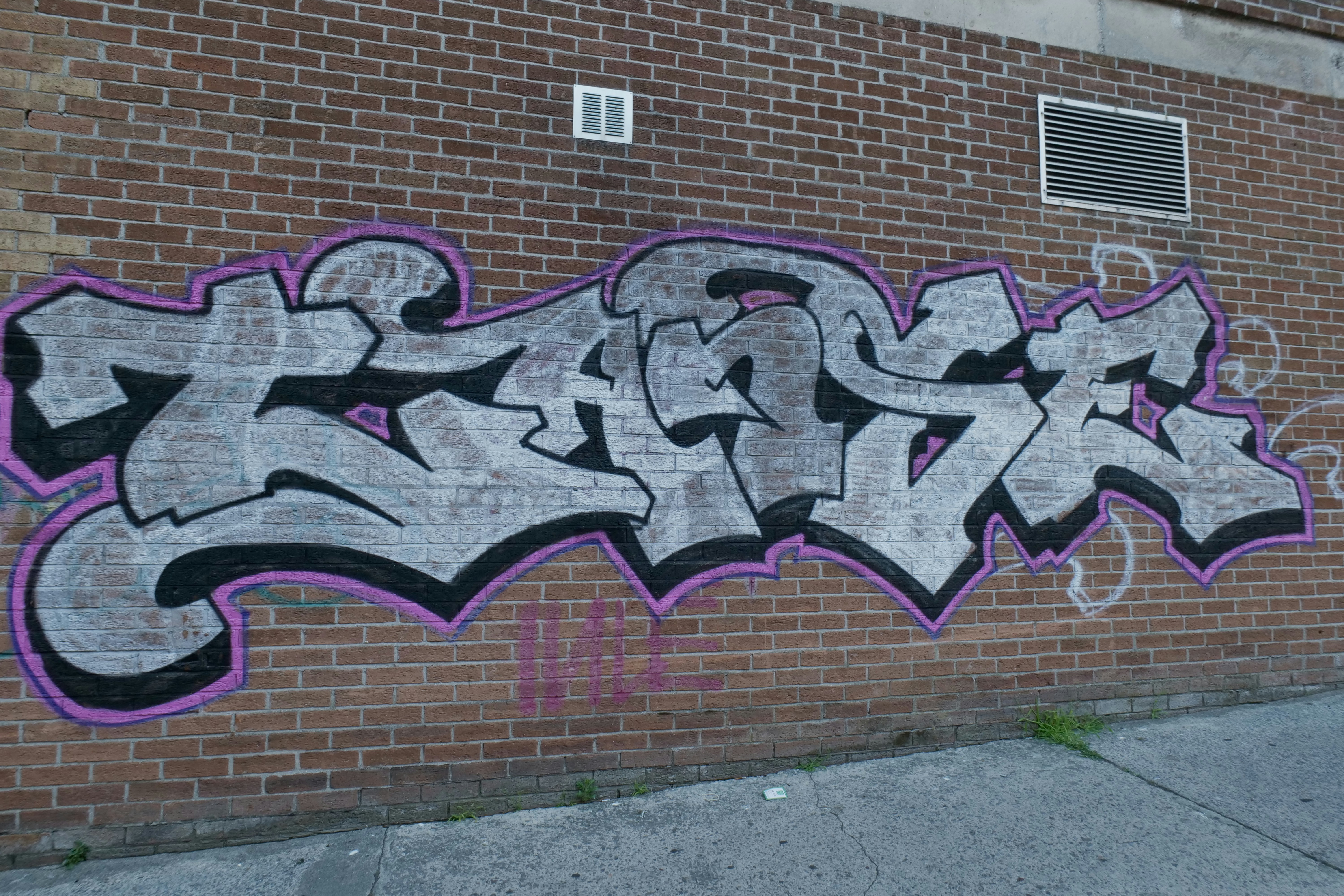 Graffiti Script on a Brick Wall: Silver Letters with Purple Outline