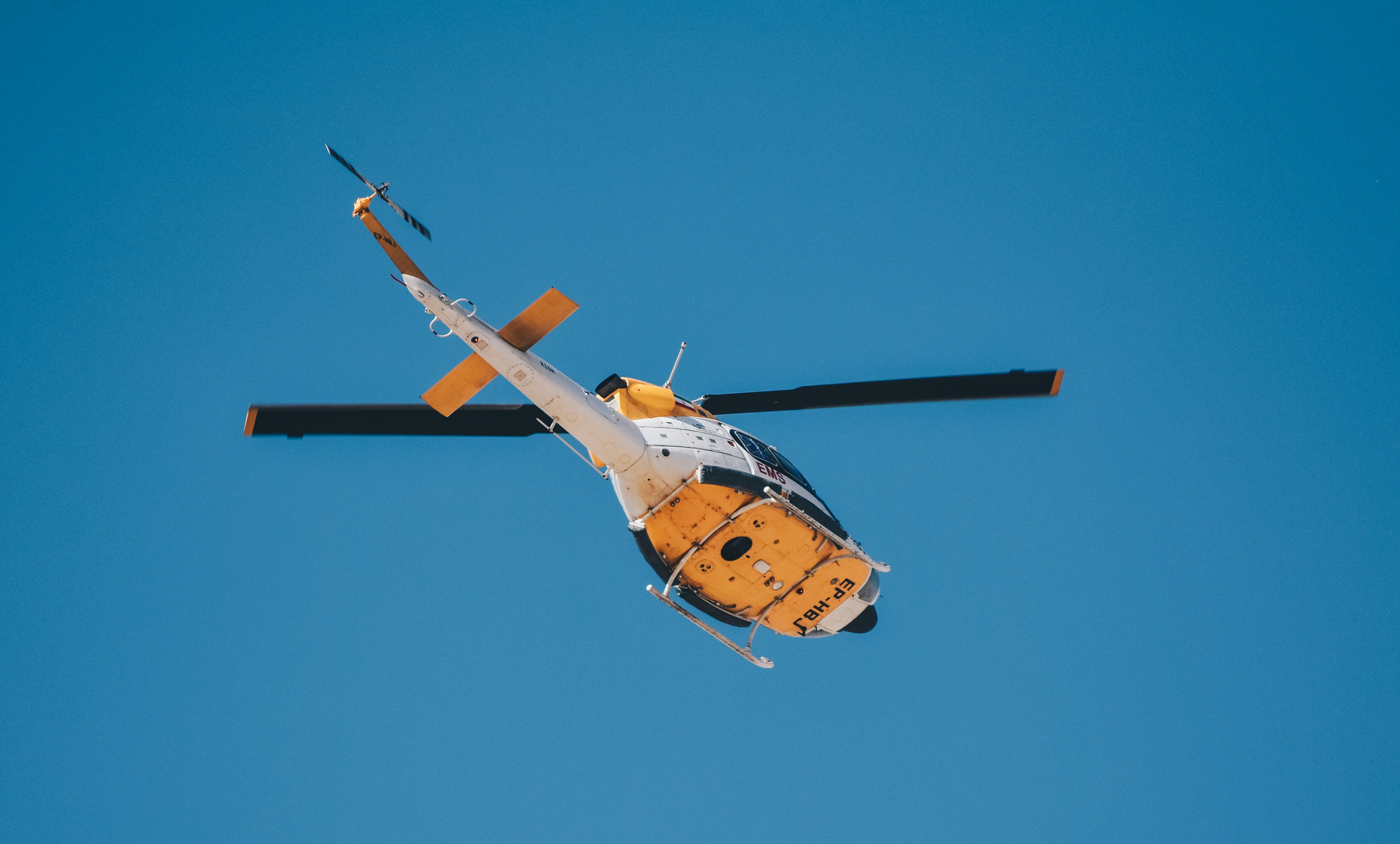 Orange-and-white rescue helicopter slicing through a clear blue sky
