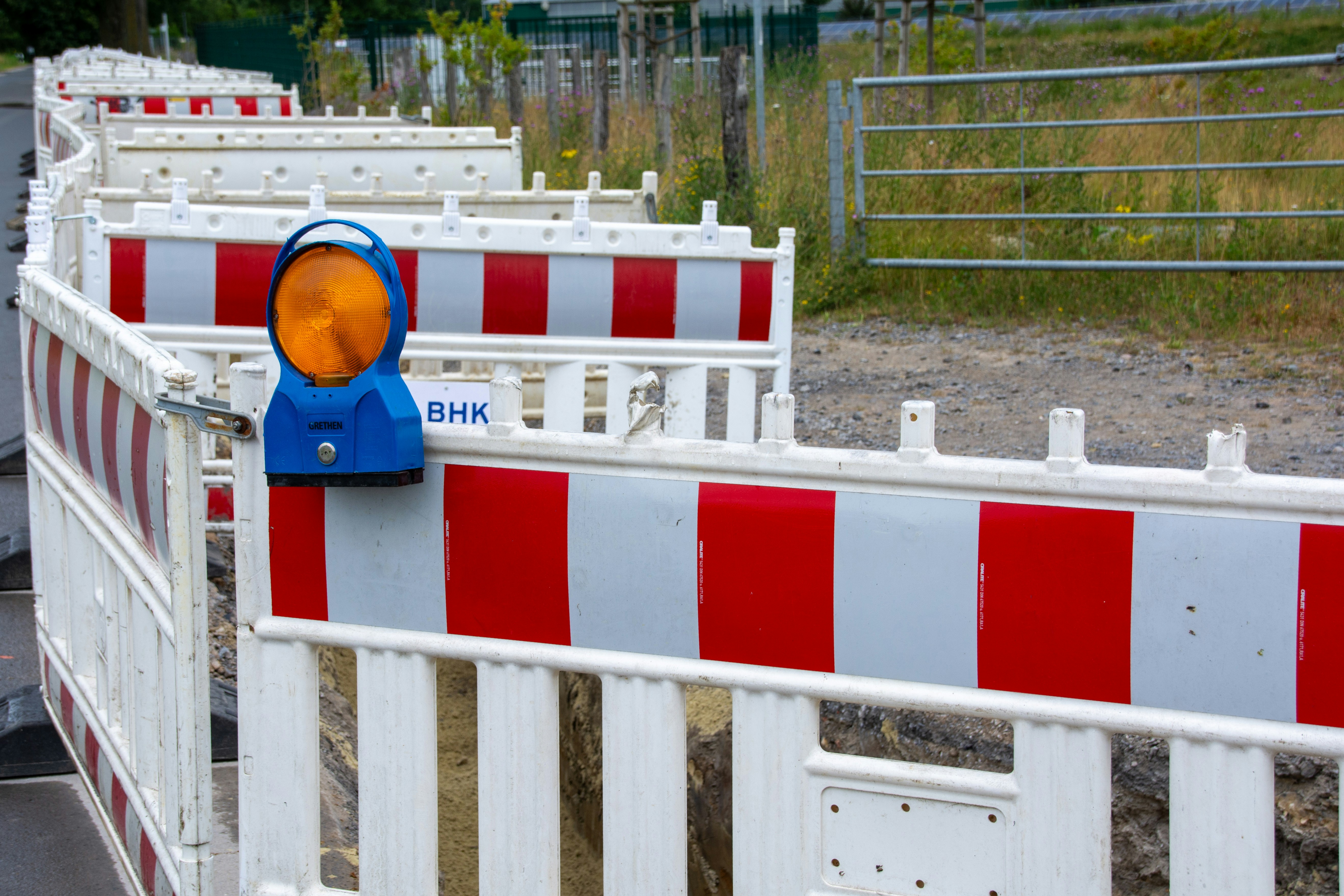 Orange Beacon Over White-and-Red Barriers on a Construction Path