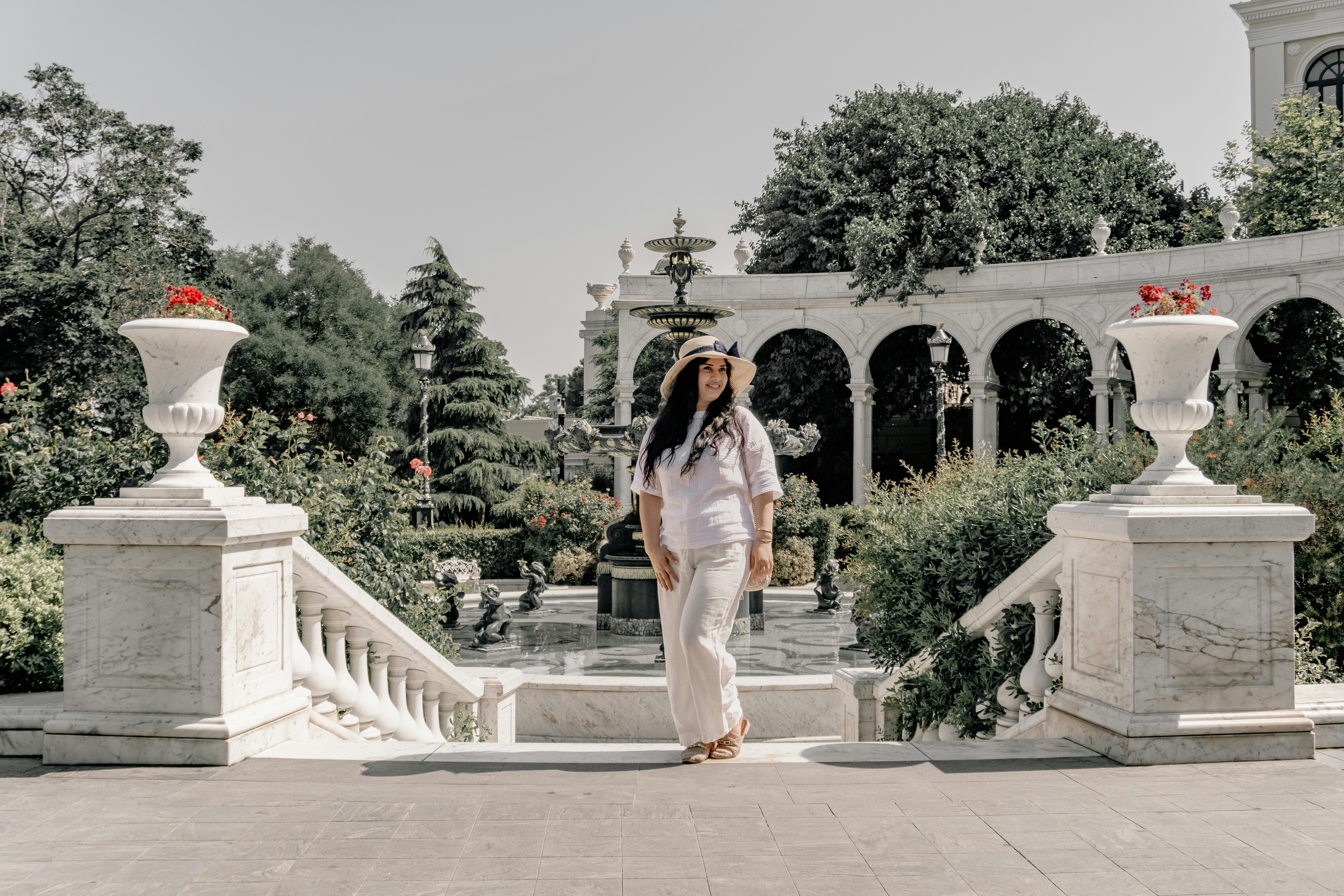 Woman in white dress at sunlit marble terrace with classical arches