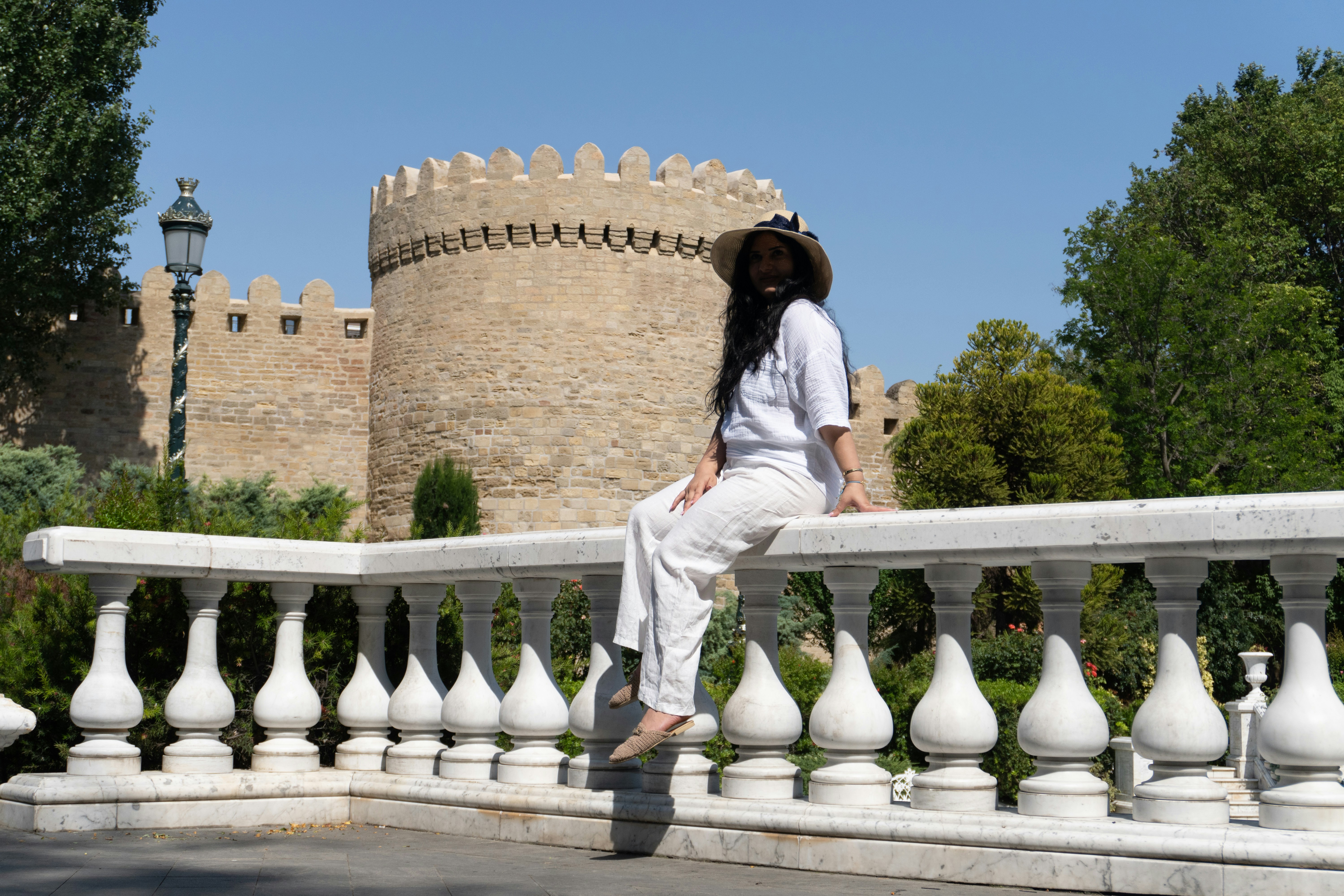 White-robed Traveler Seated on a Marble Balustrade Before a Historic Keep