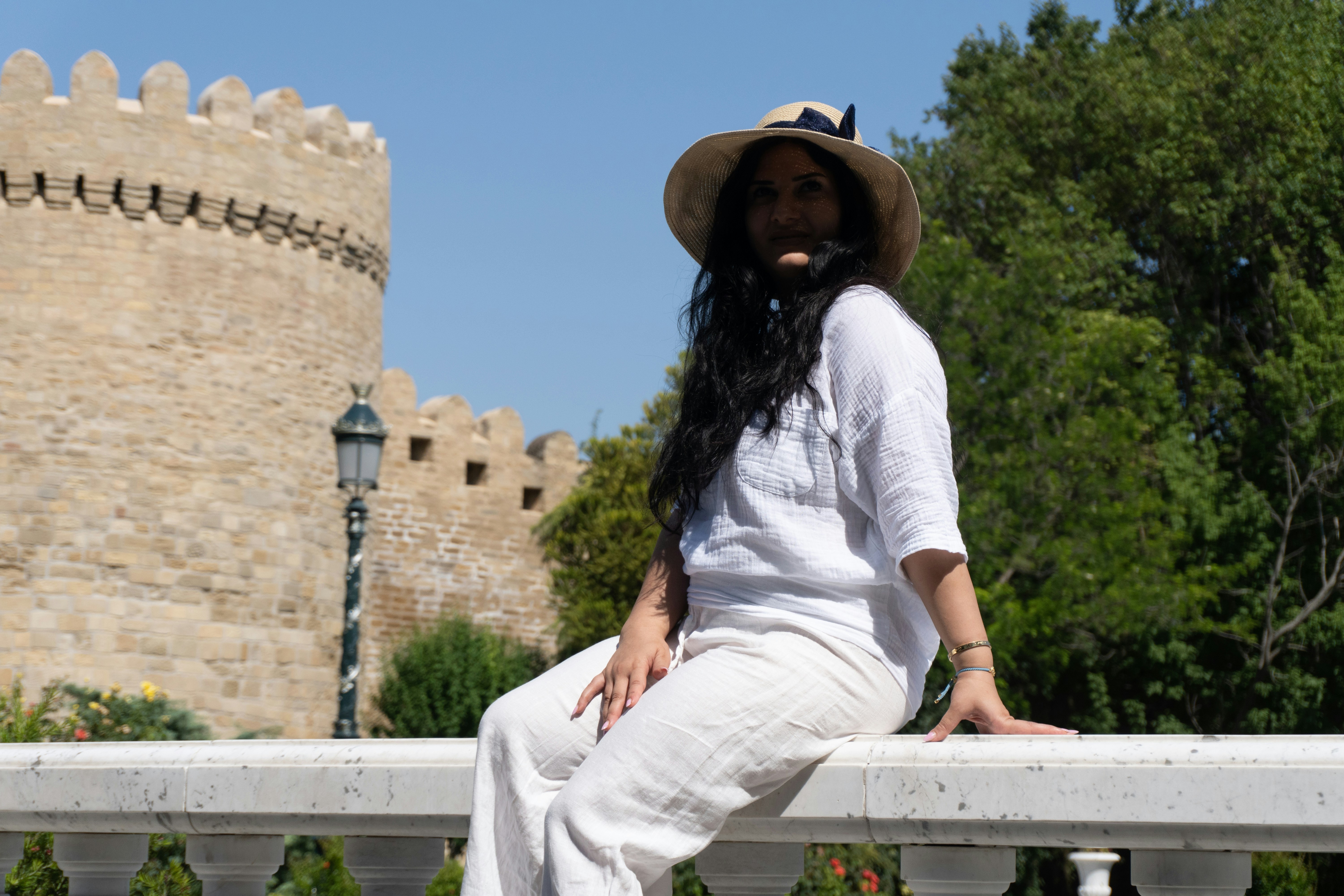 Sunlit Serenity: A Woman in White Beside Ancient Walls