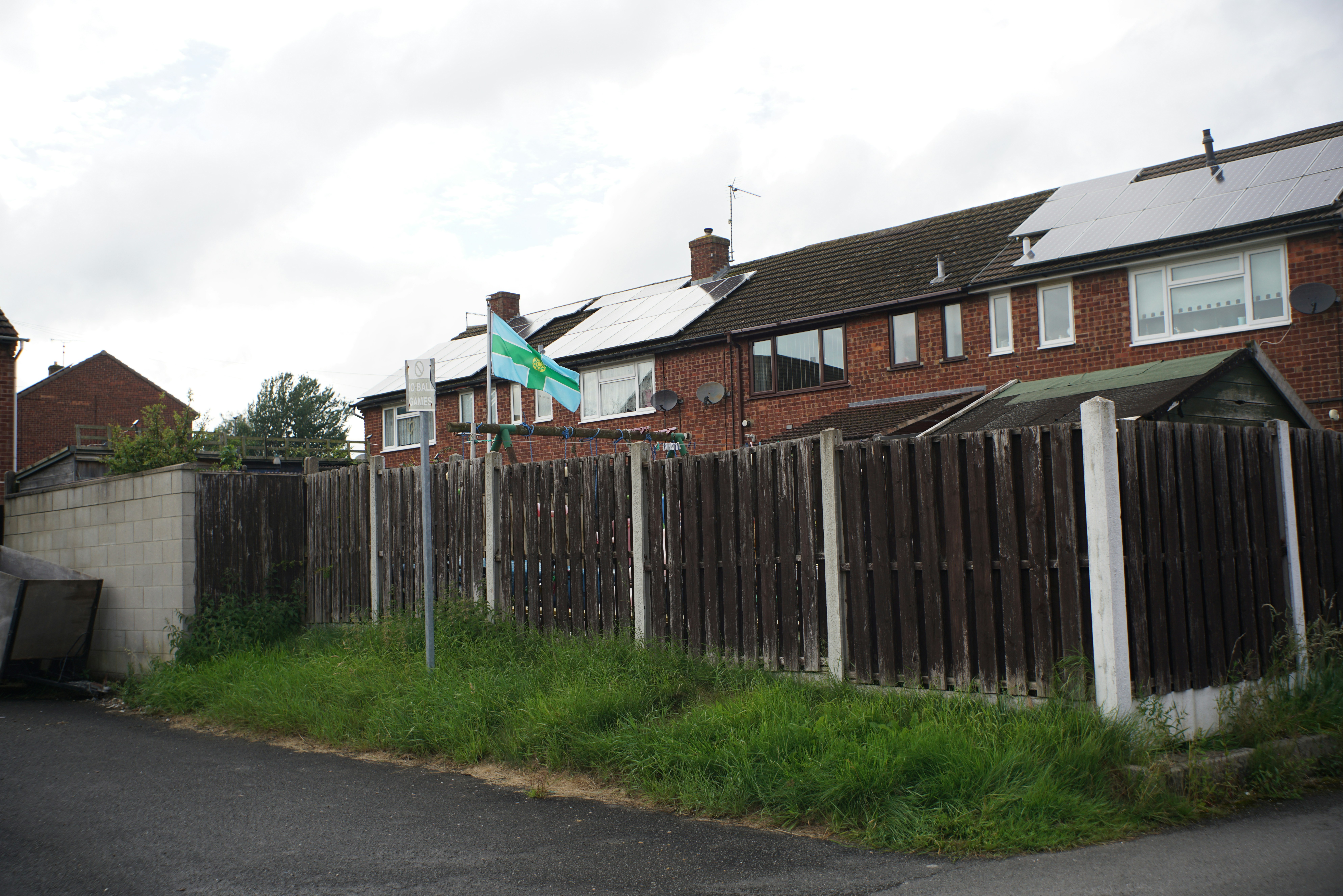 Dilapidated fence line and brick row houses under a cloudy sky