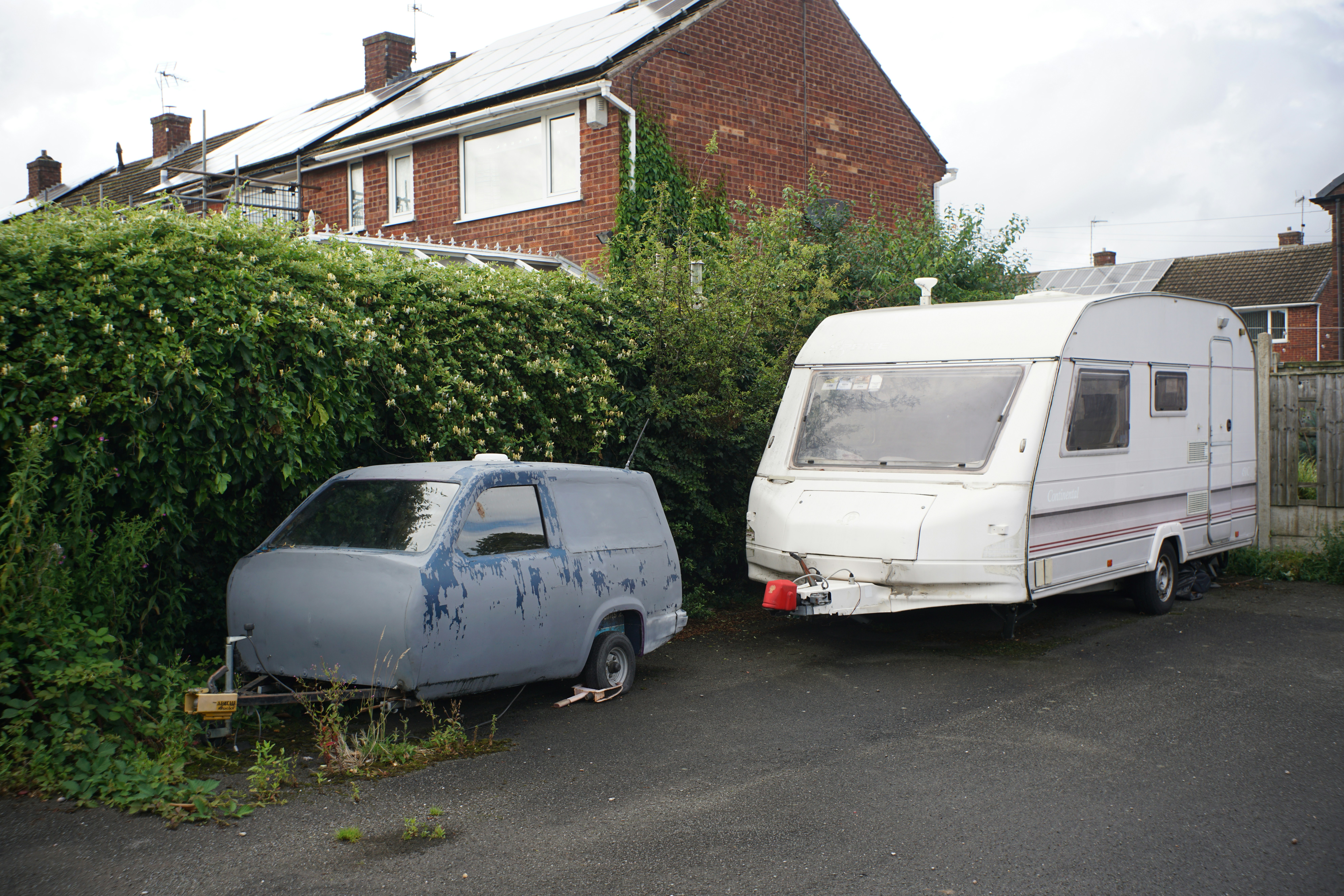 Abandoned caravan and vintage trailer tucked beside a hedge