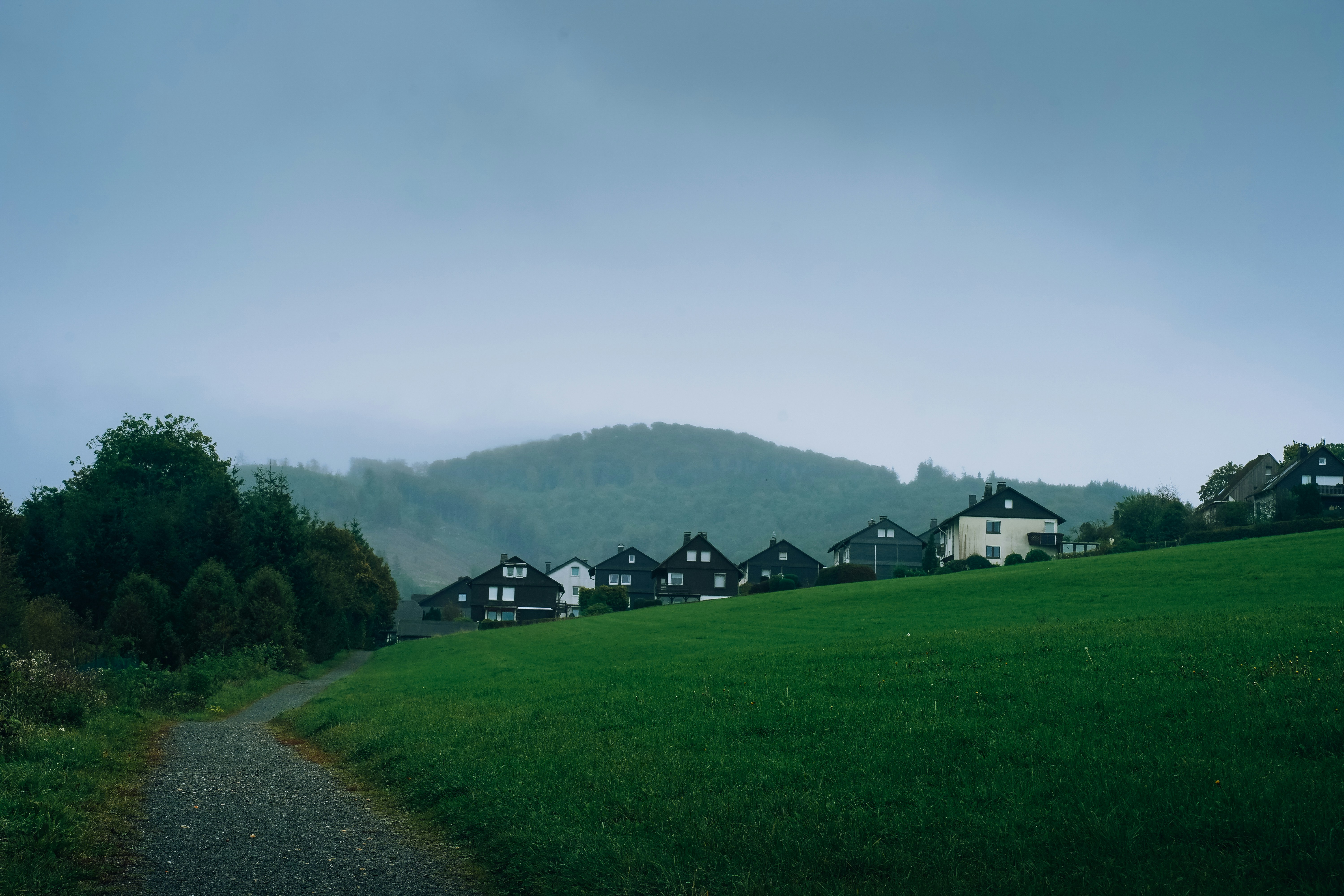 Row of white houses perched along a grassy hillside under a misty blue sky