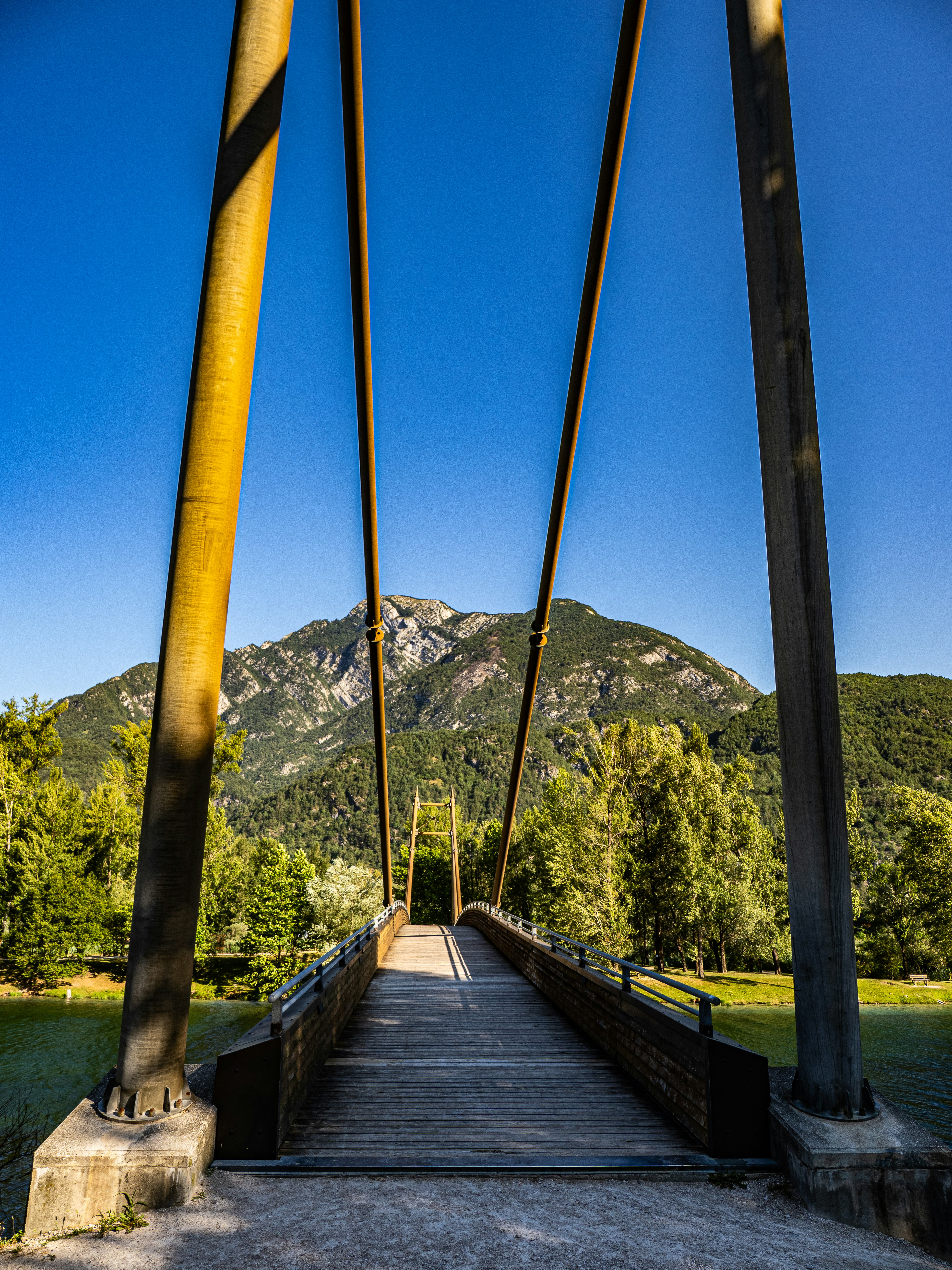 Suspended Corridor: A Wooden Bridge Framed by Tall Steel Beams Before a Mountain Vale