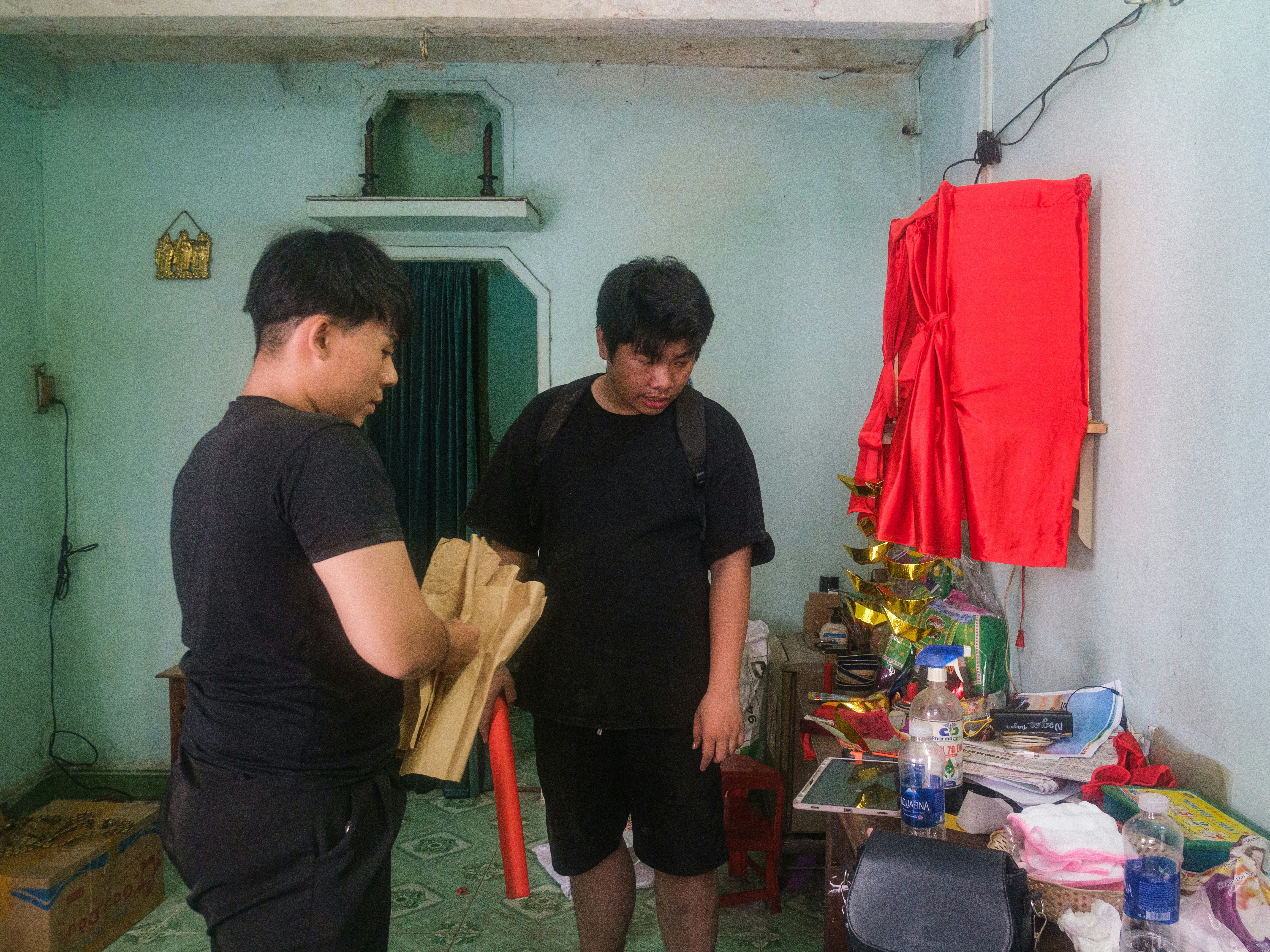 Two men prepping a humble room for delivery amidst scattered goods