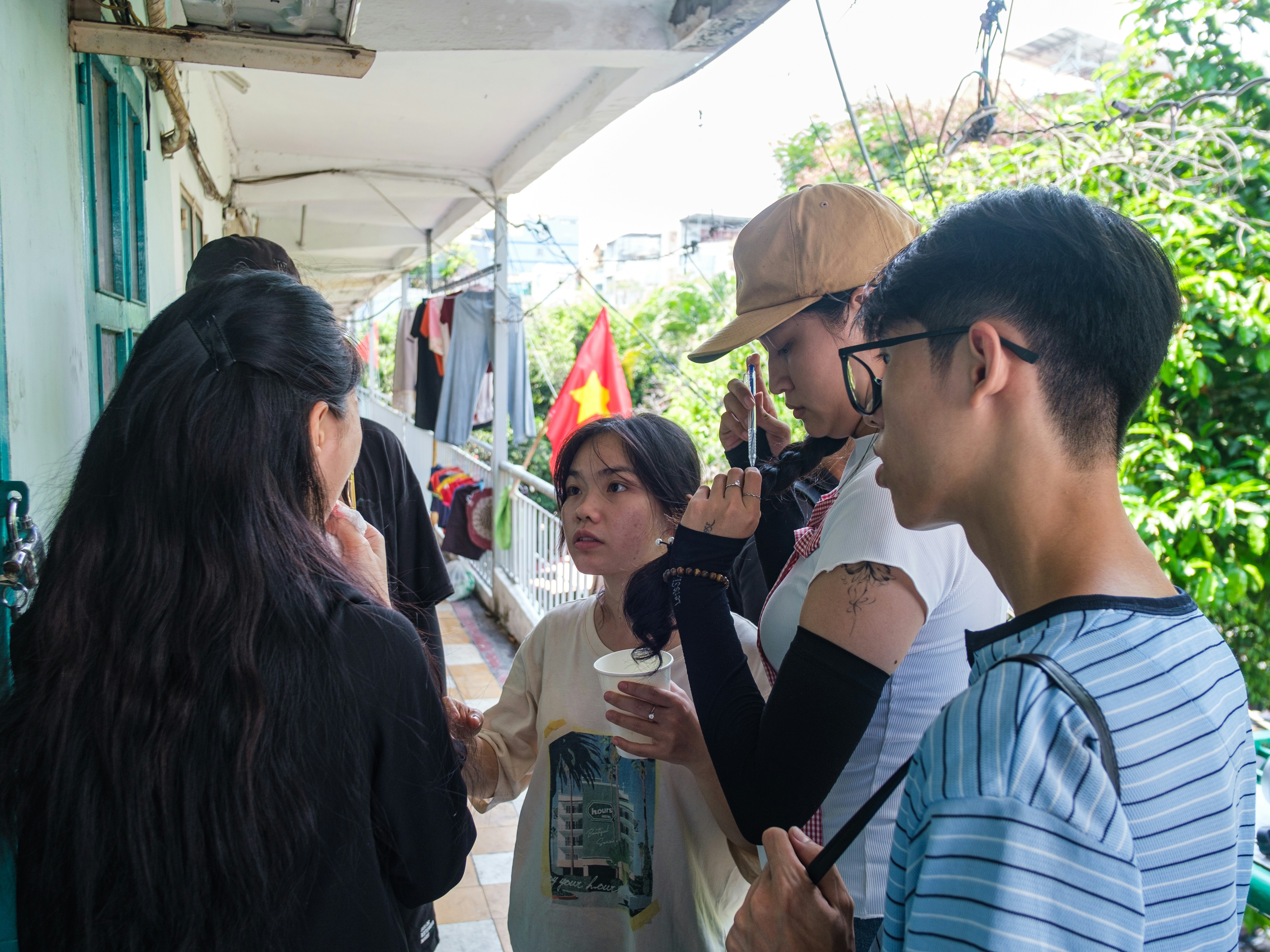 Mid-conversation in a sunlit alleyway with a Vietnamese flag in the background