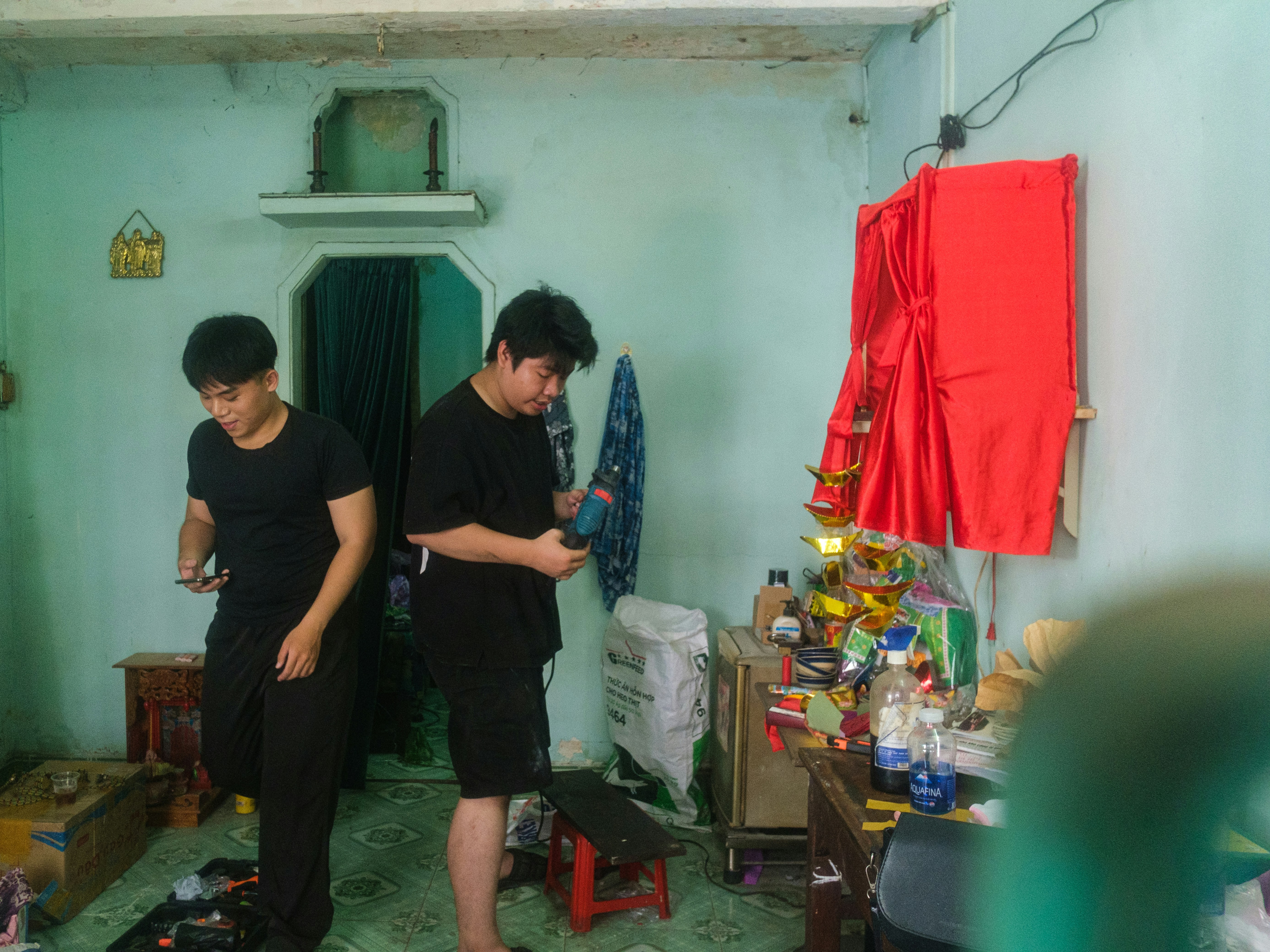 Two Friends in a Modest Shrine Room Adjusting Objects