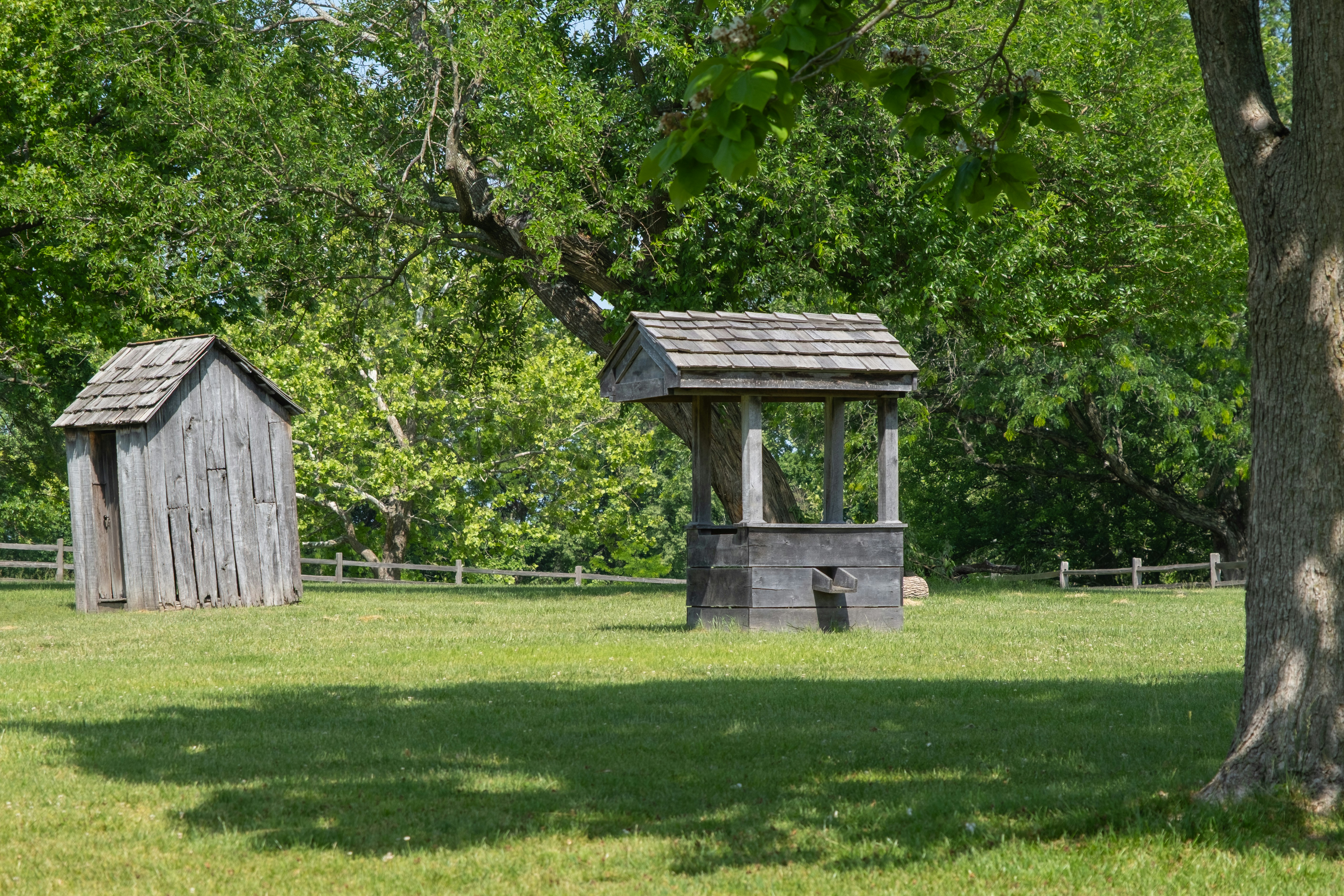 Pastoral Stillness: Weathered Wells and Wooden Sheds in a Sunlit Clearing