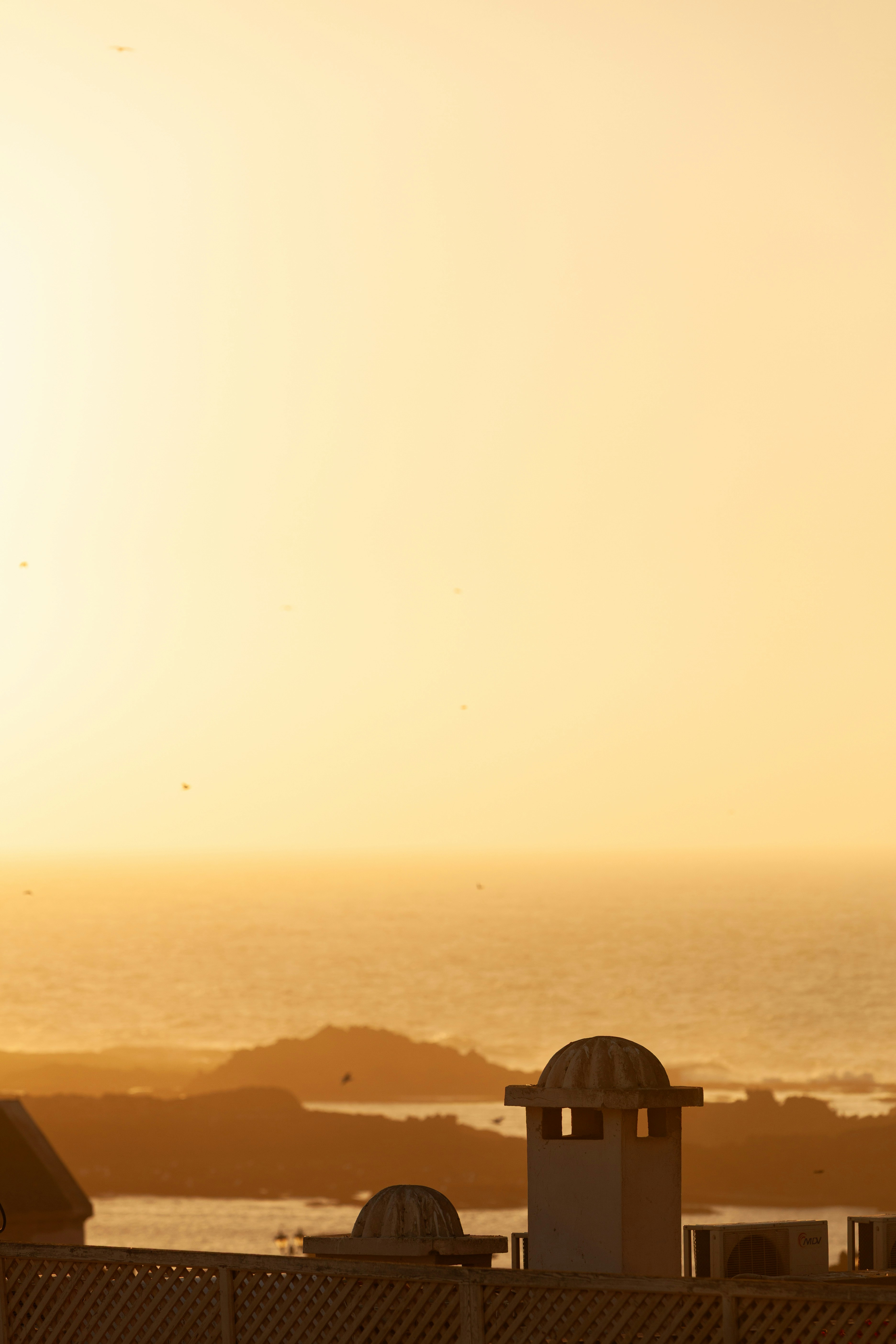 Halo on the Horizon: Rooftops Framing a Seaside Sunset