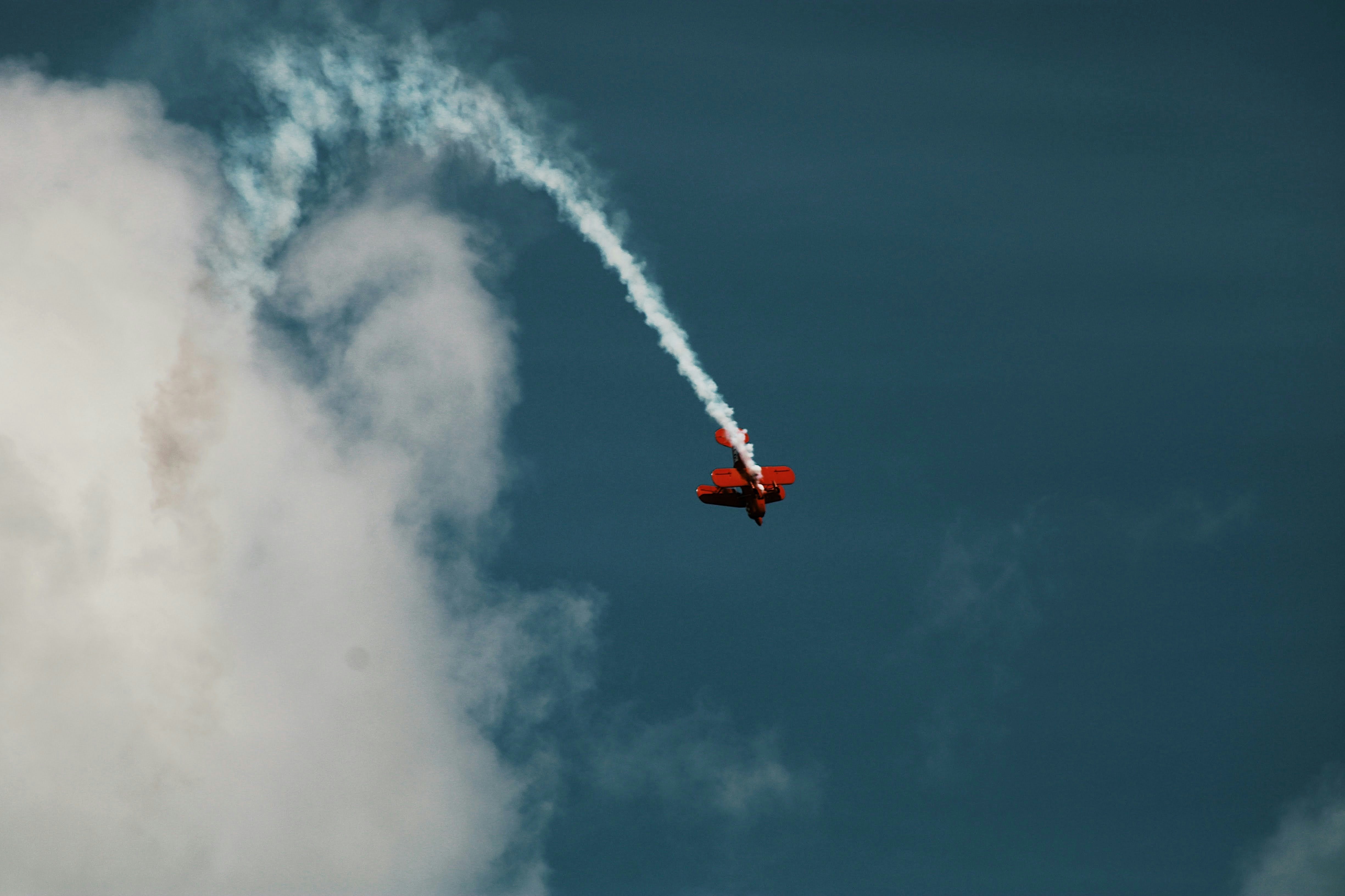 Red Biplane Tracing a Smoke Arc Against a Vast Sky