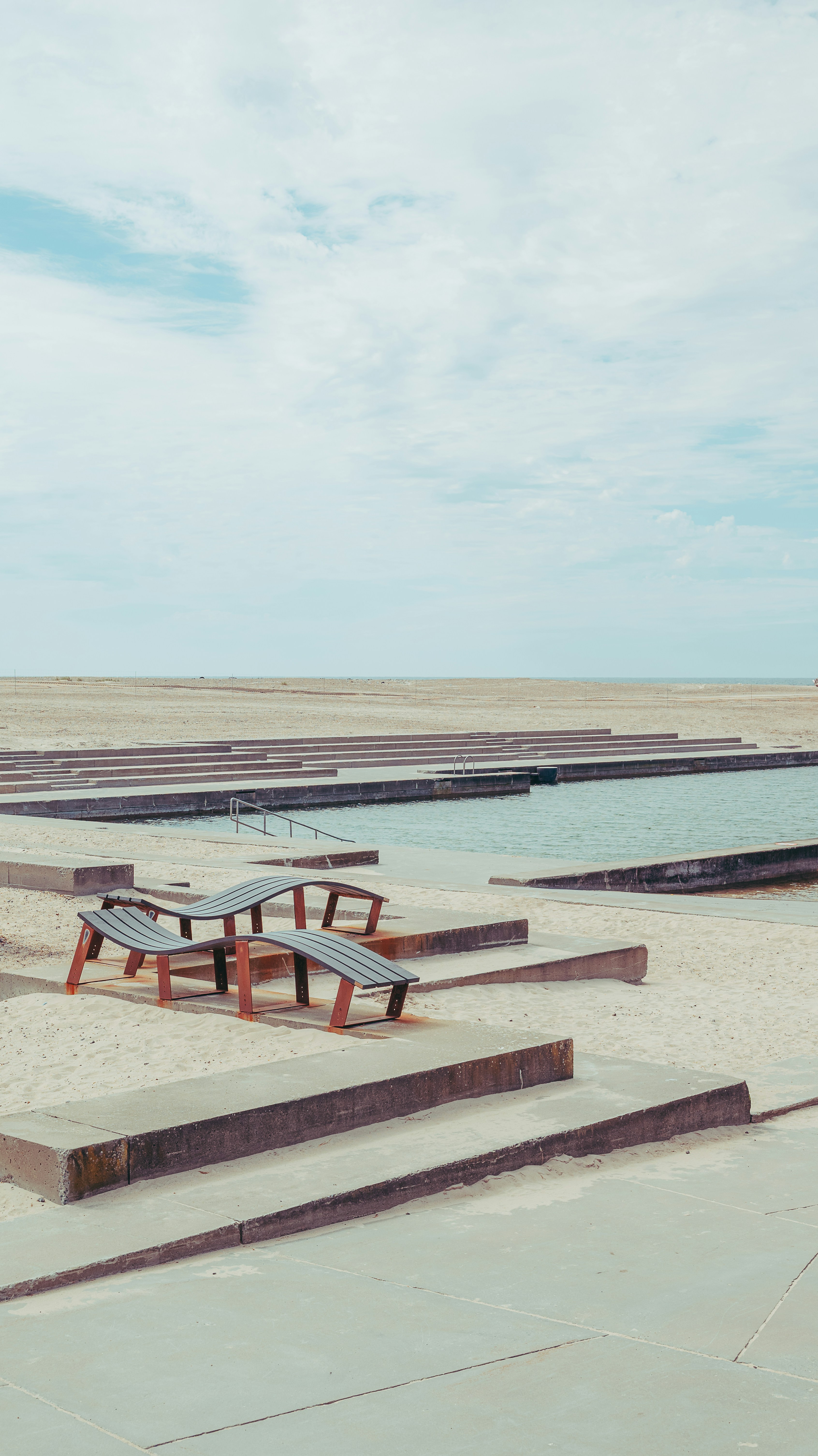 Quiet seaside terrace: wooden loungers at the edge of calm waters