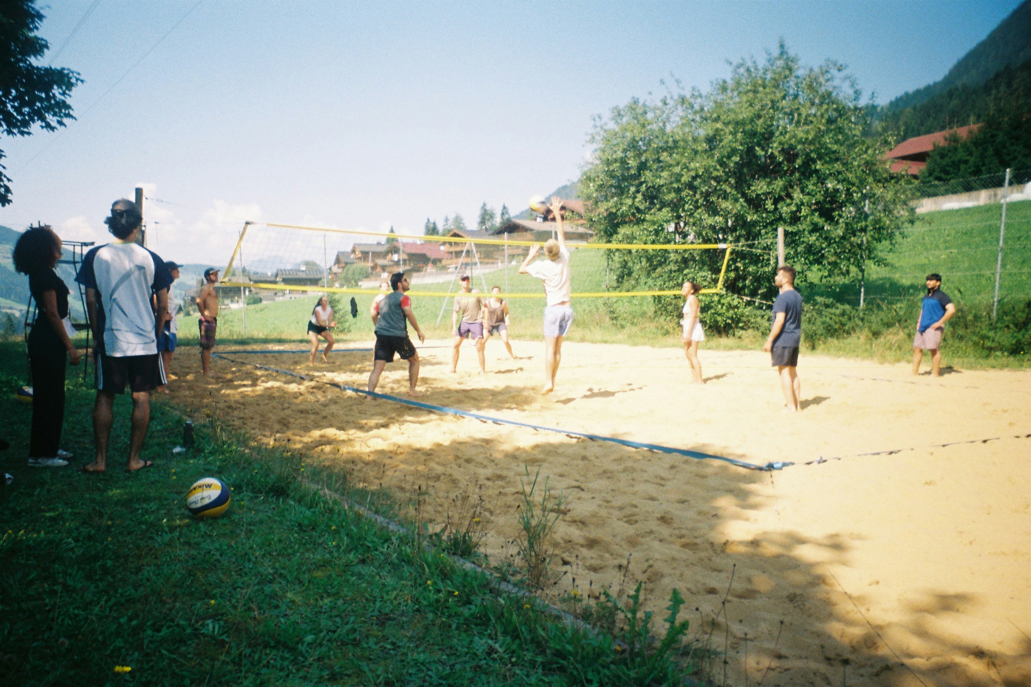 Sunlit Village Court: Teens Rally Around a Beach Volleyball Game