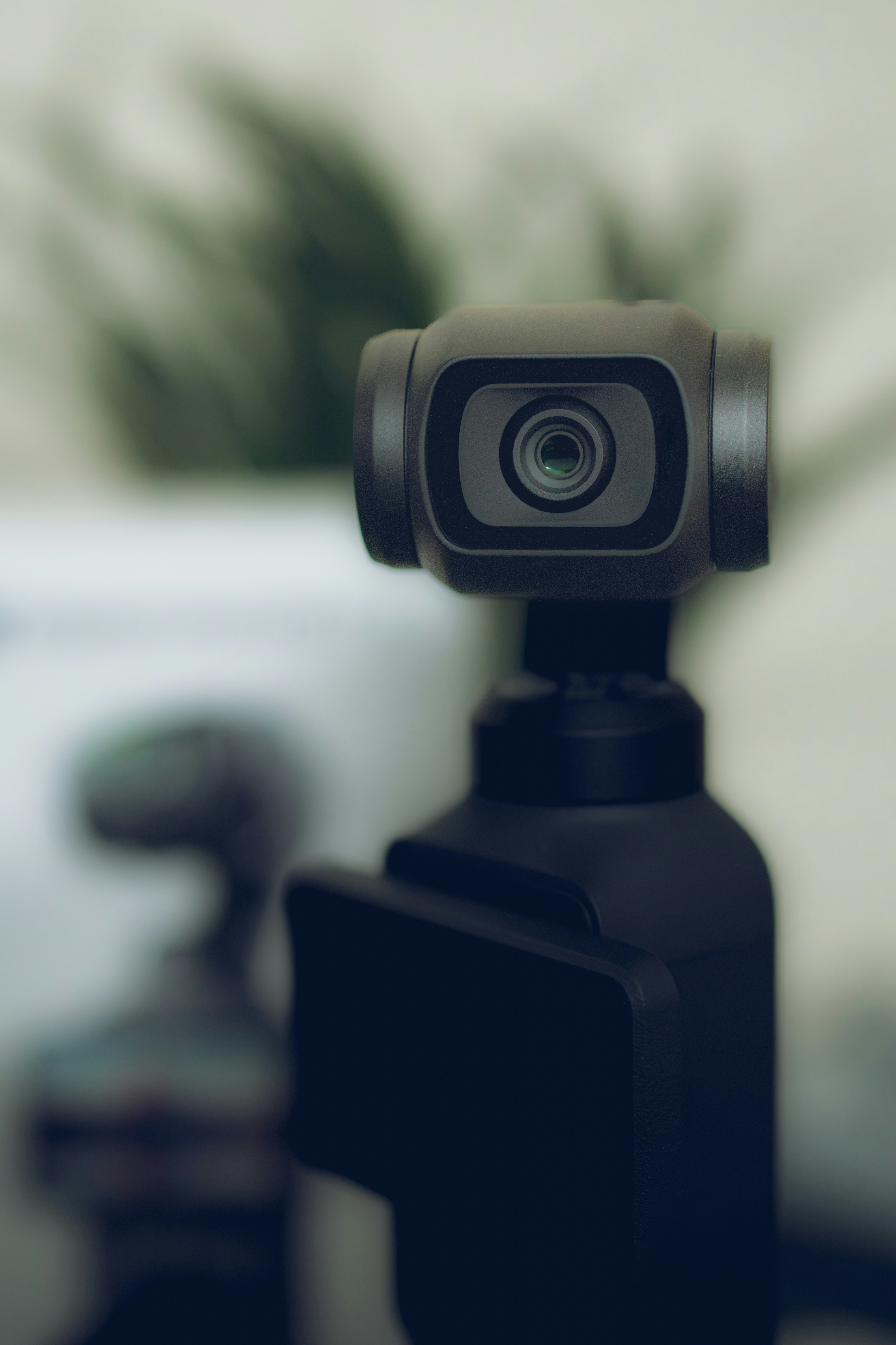 Close-up shot of a gimbal-mounted camera head with the lens centered in the frame; soft background blur emphasizes the front-facing optic. The scene appears as a product or studio setup with a shallow depth-of-field, highlighting the device’s front elements.
