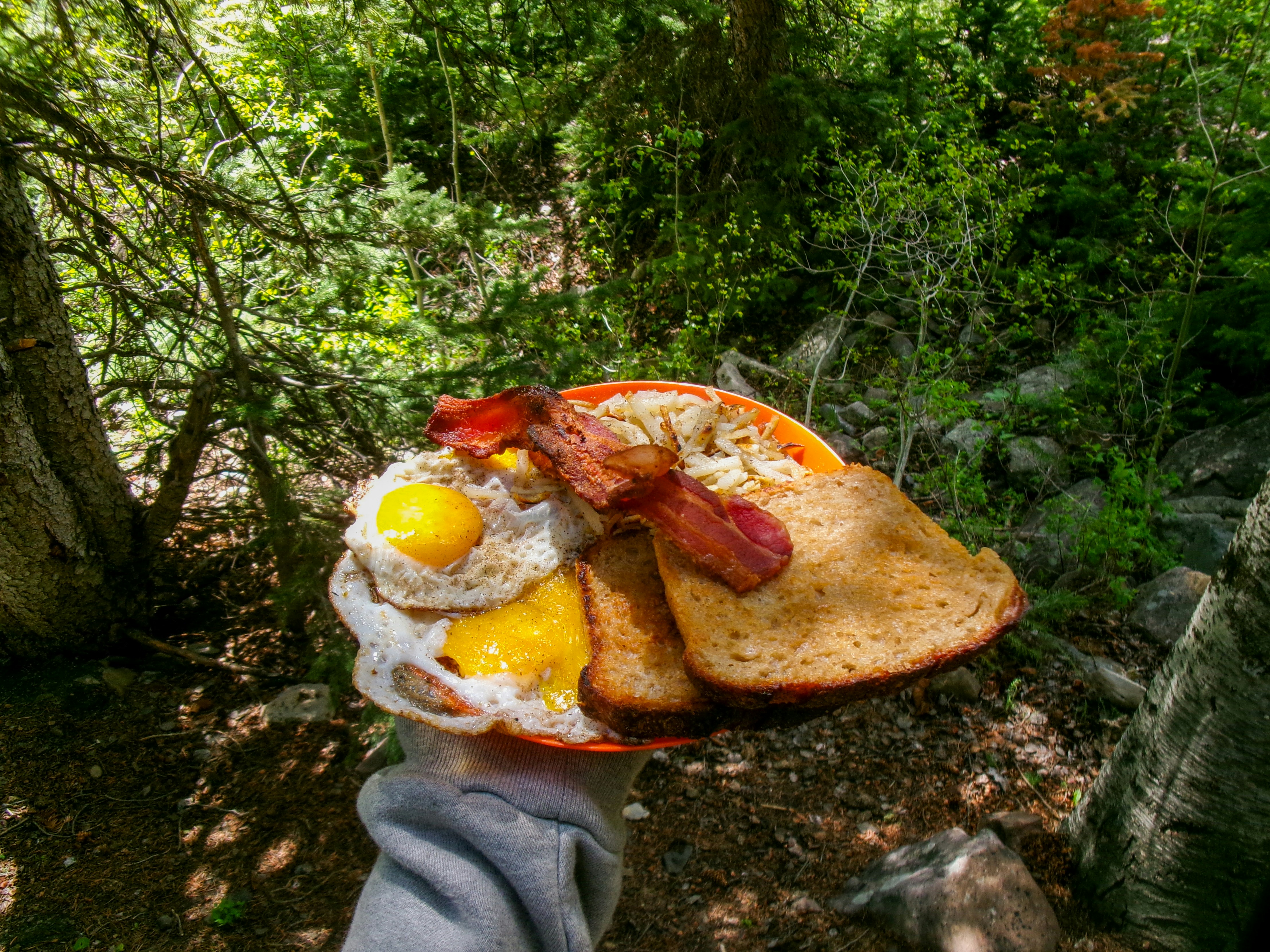 Outdoor breakfast on a rustic plate: sunny side up with bacon and toast