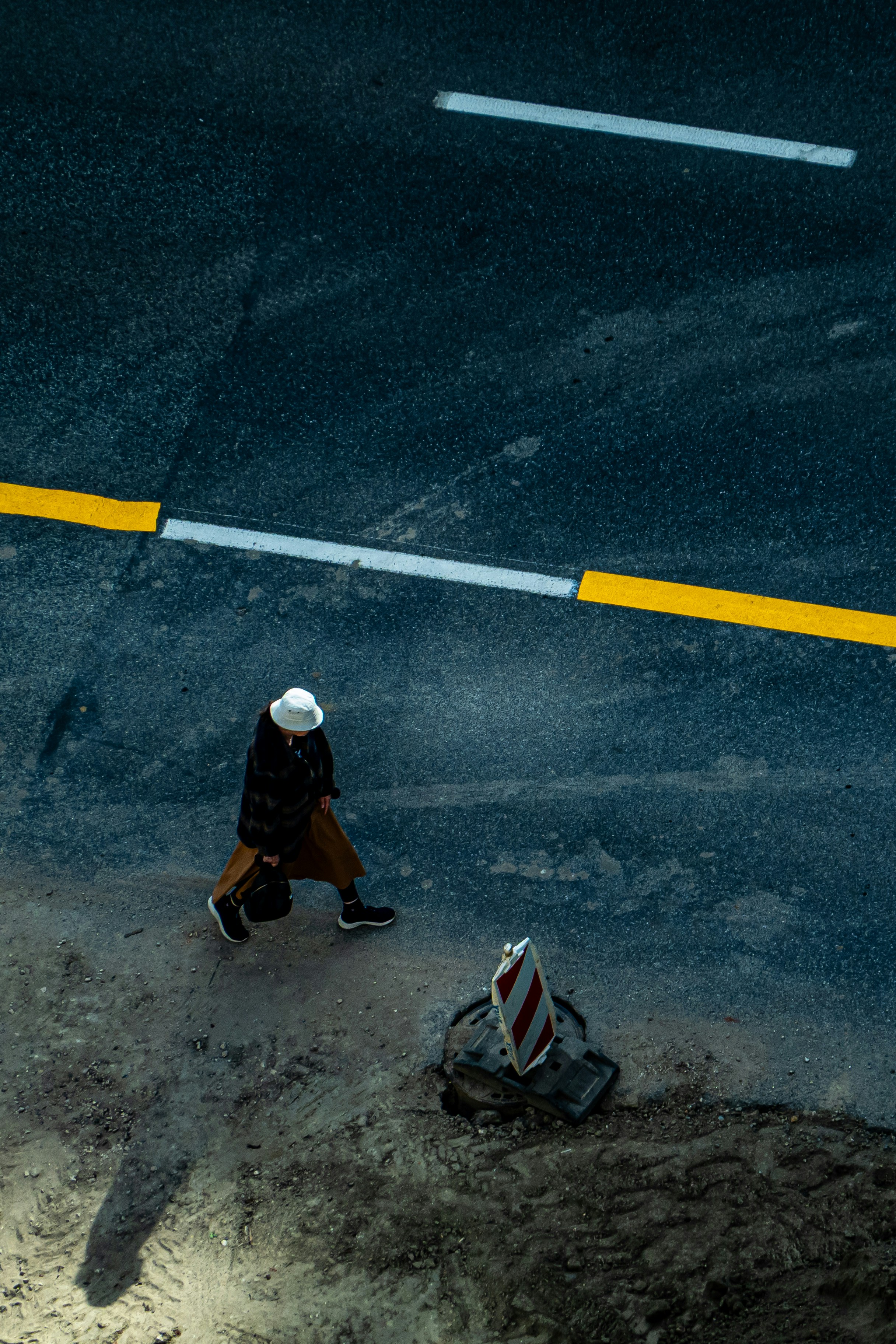Urban Silhouette: Pedestrian Traverses a Painted Road Between Striped Barriers