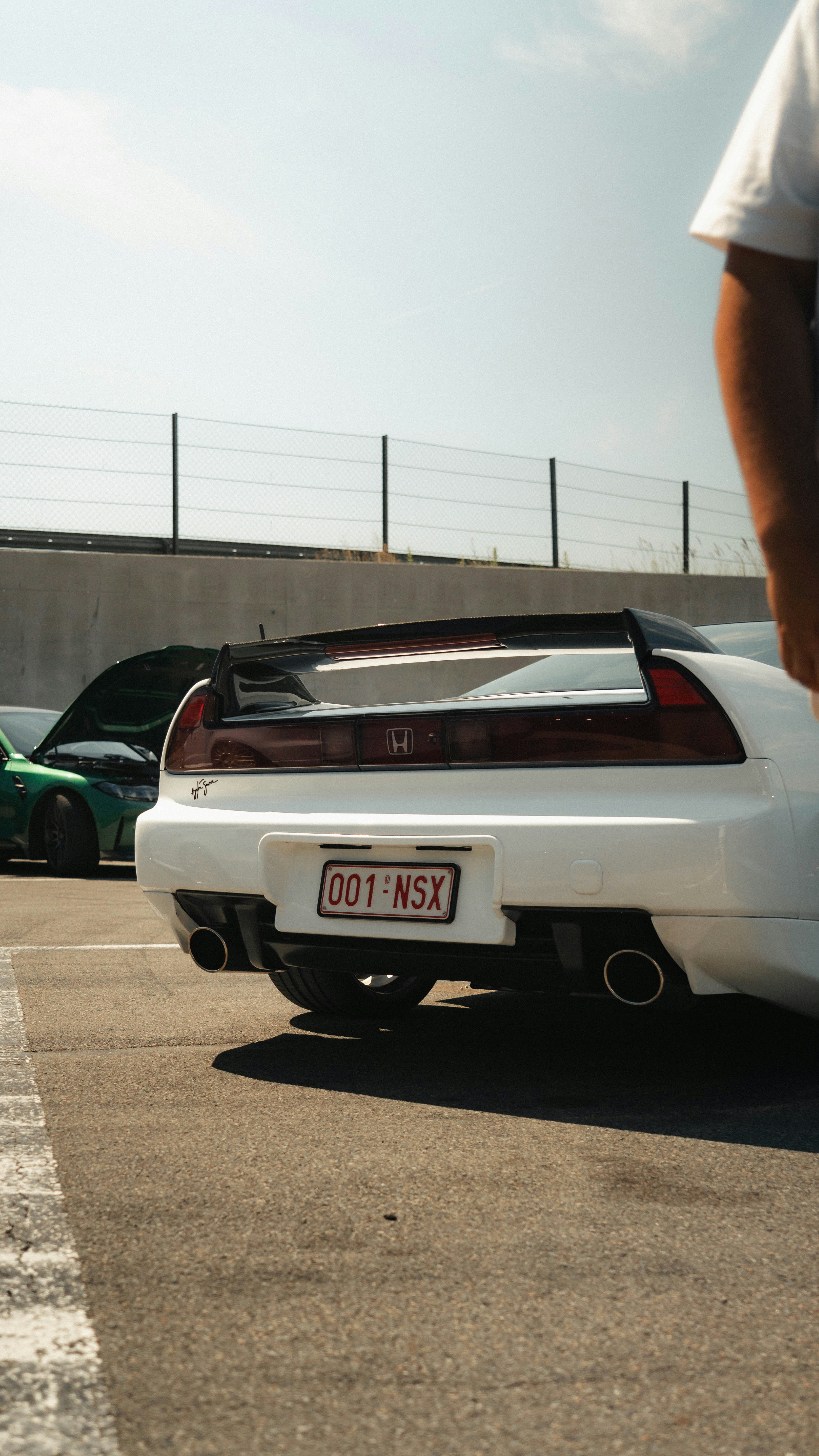 Rear Halo: A white sports coupe with a bold spoiler in a sunlit parking lot