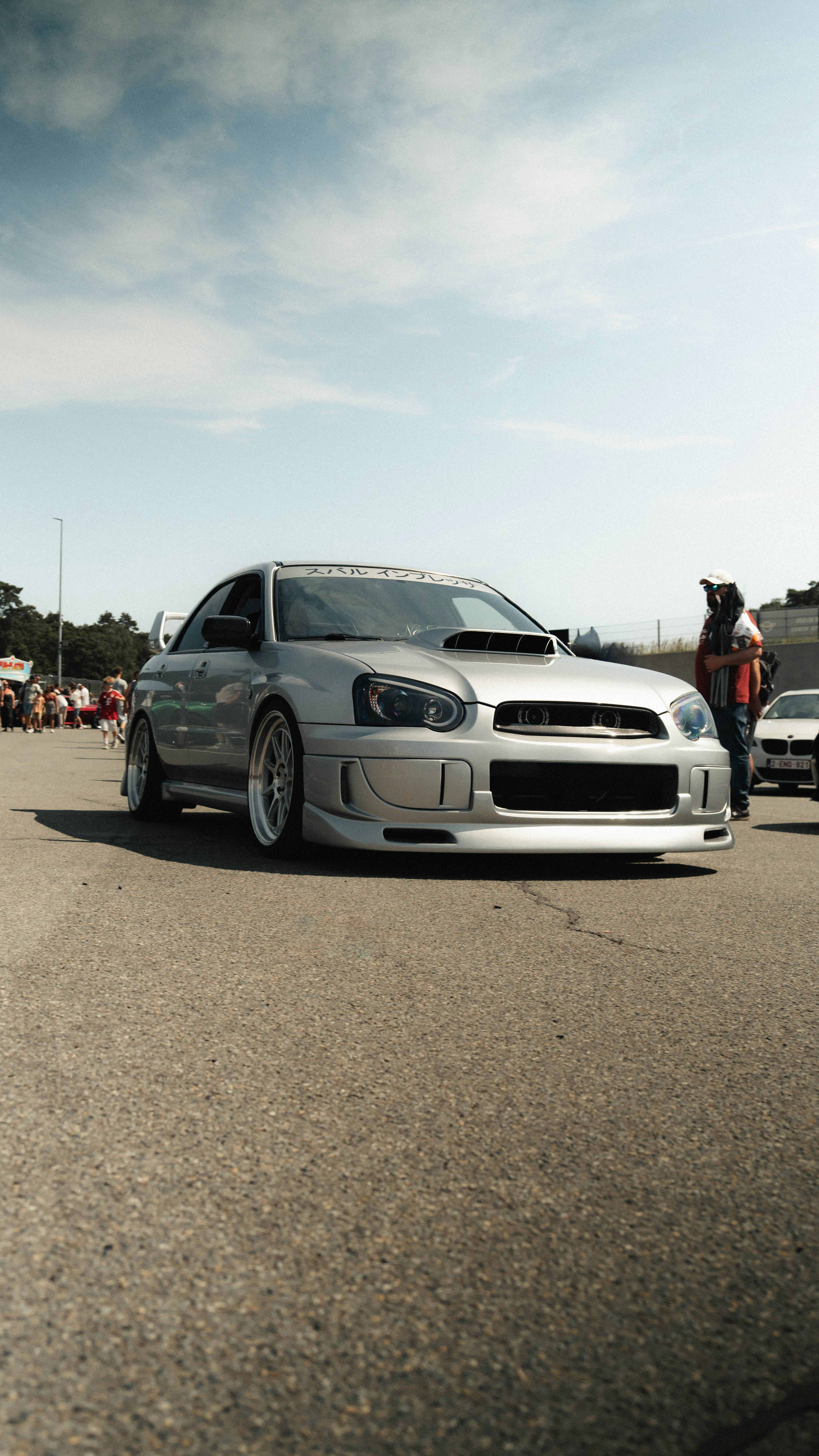Low-slung silver sedan at a sunny car meet, front-and-center on the track