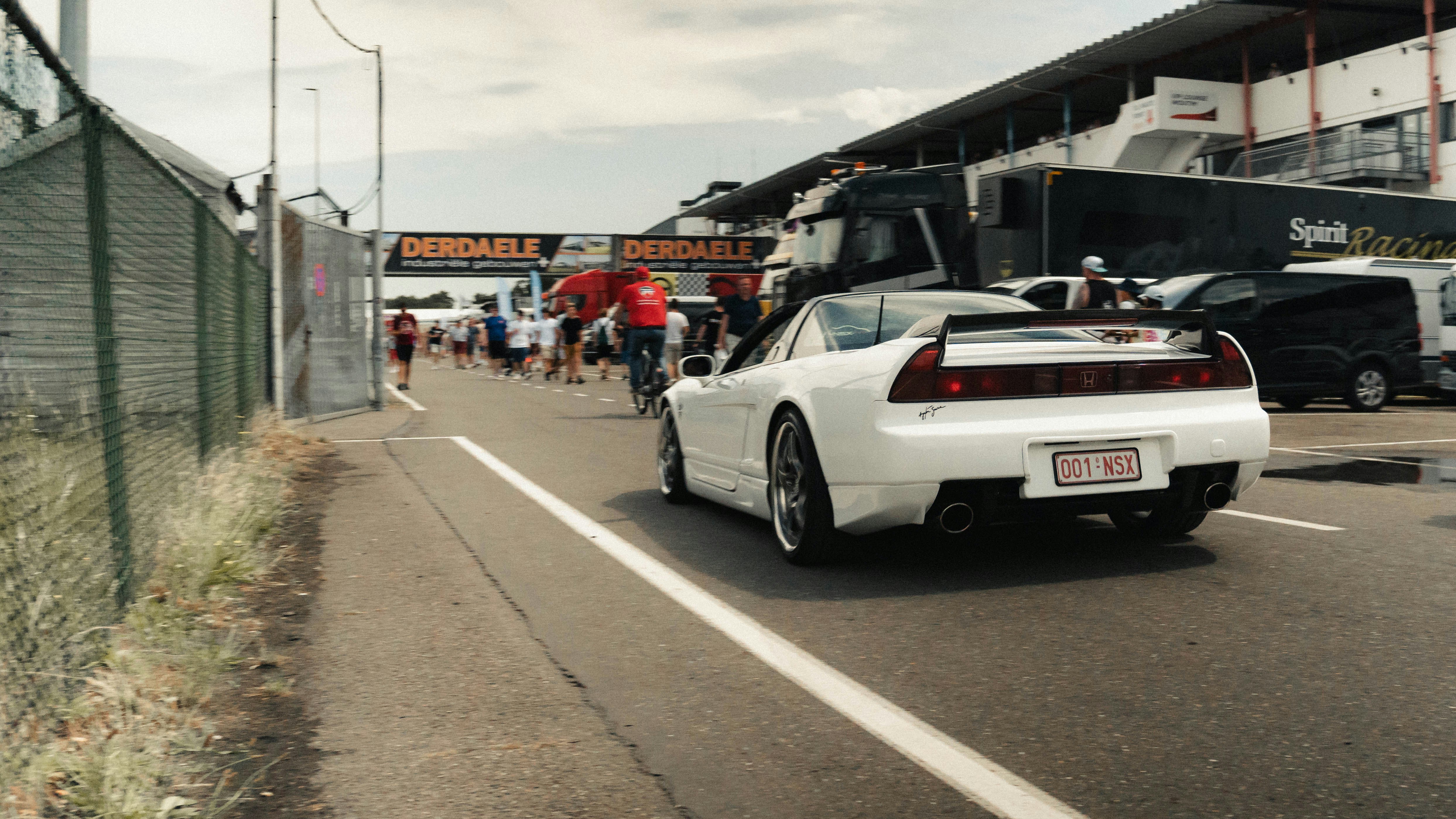 White sports car leads the pit lane parade under racing banners