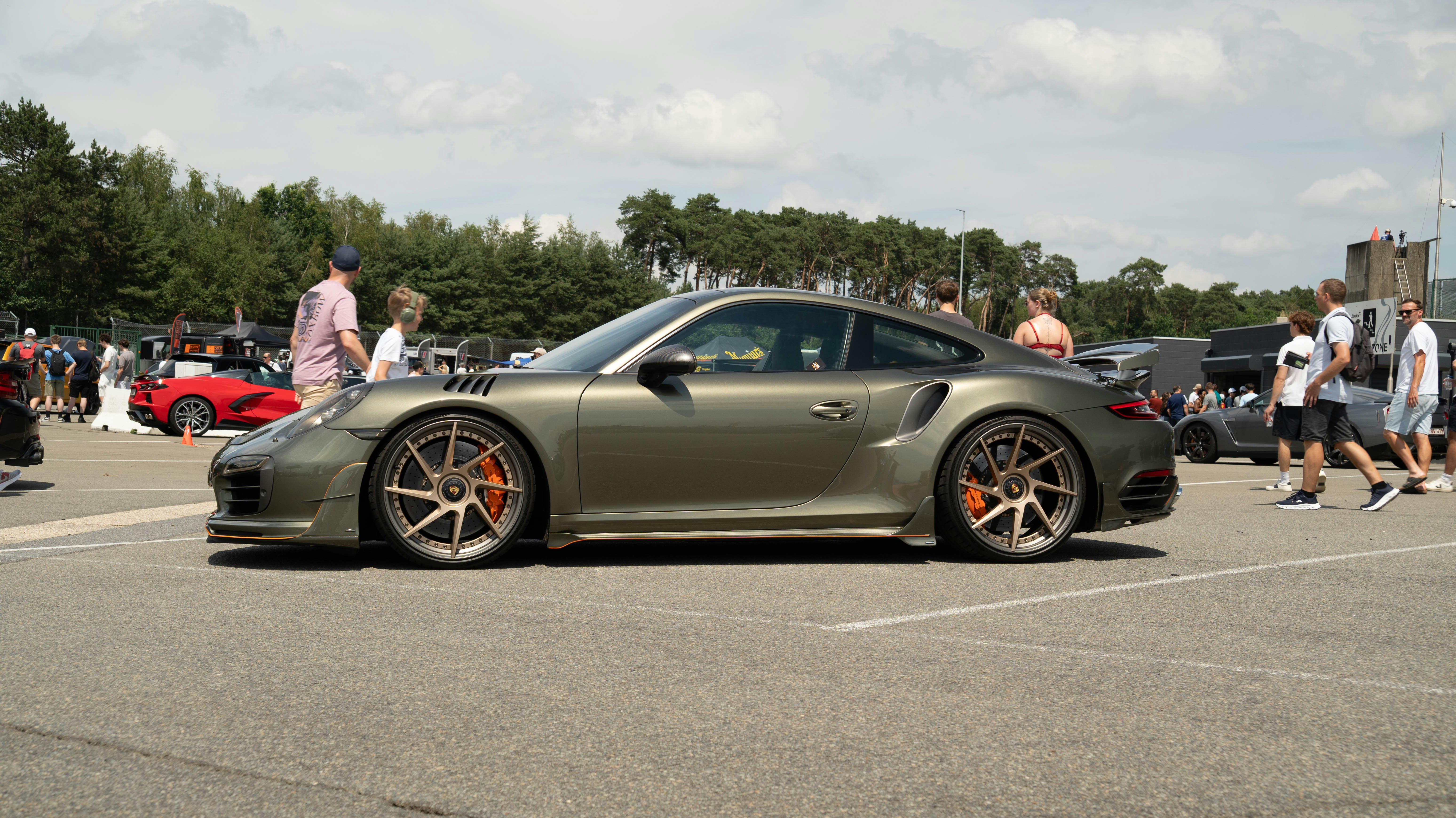 Matte-green Porsche with gold wheels anchors a casual car-show scene