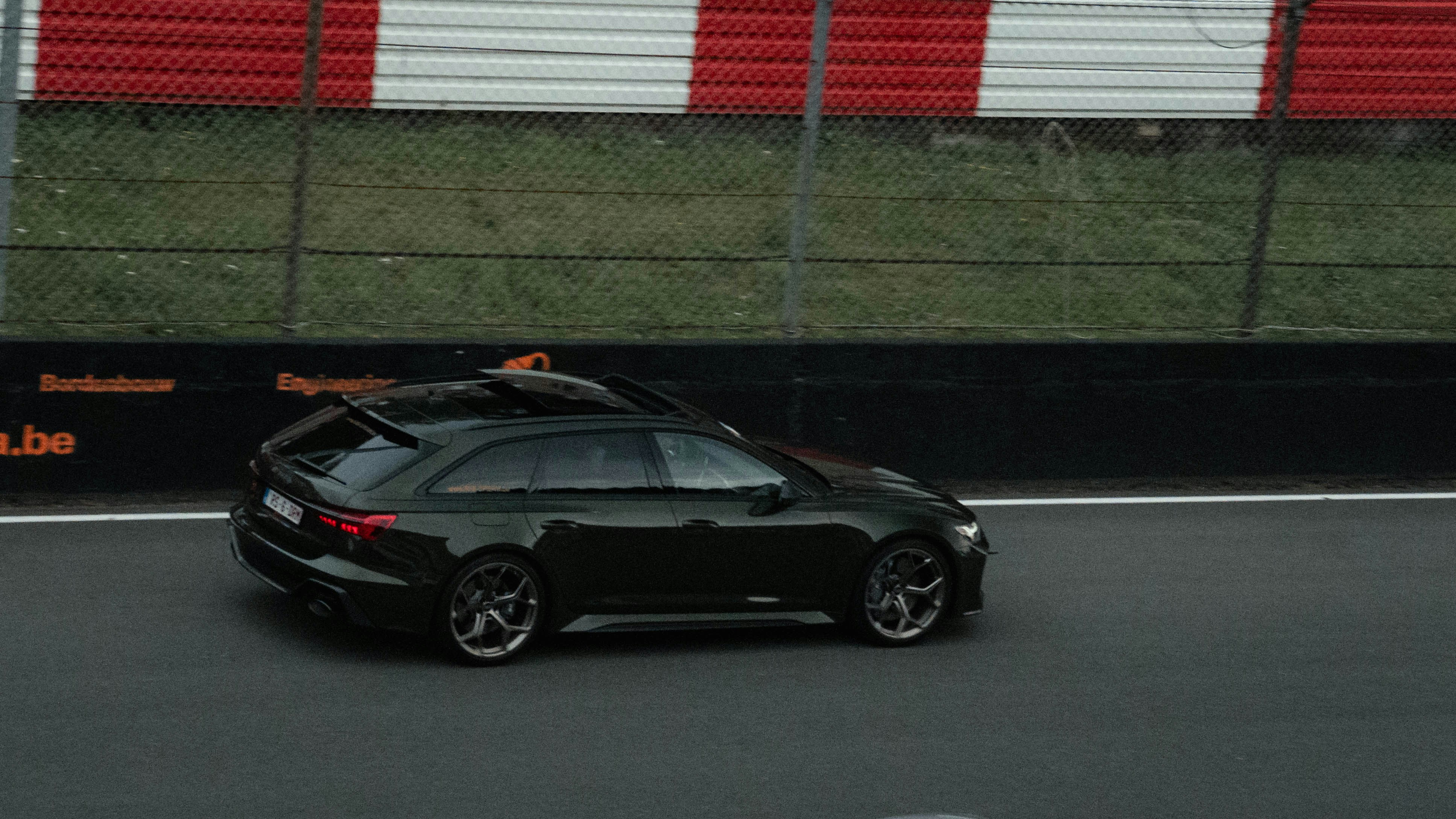 Black sport sedan slices along the track under a chain-link backdrop
