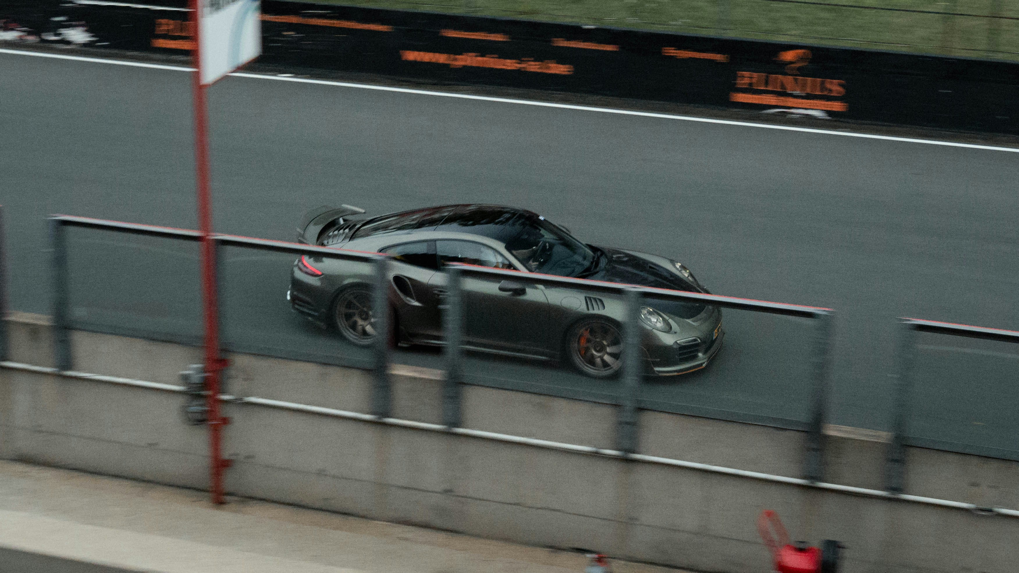 A dark grey sports car drives on a race track.