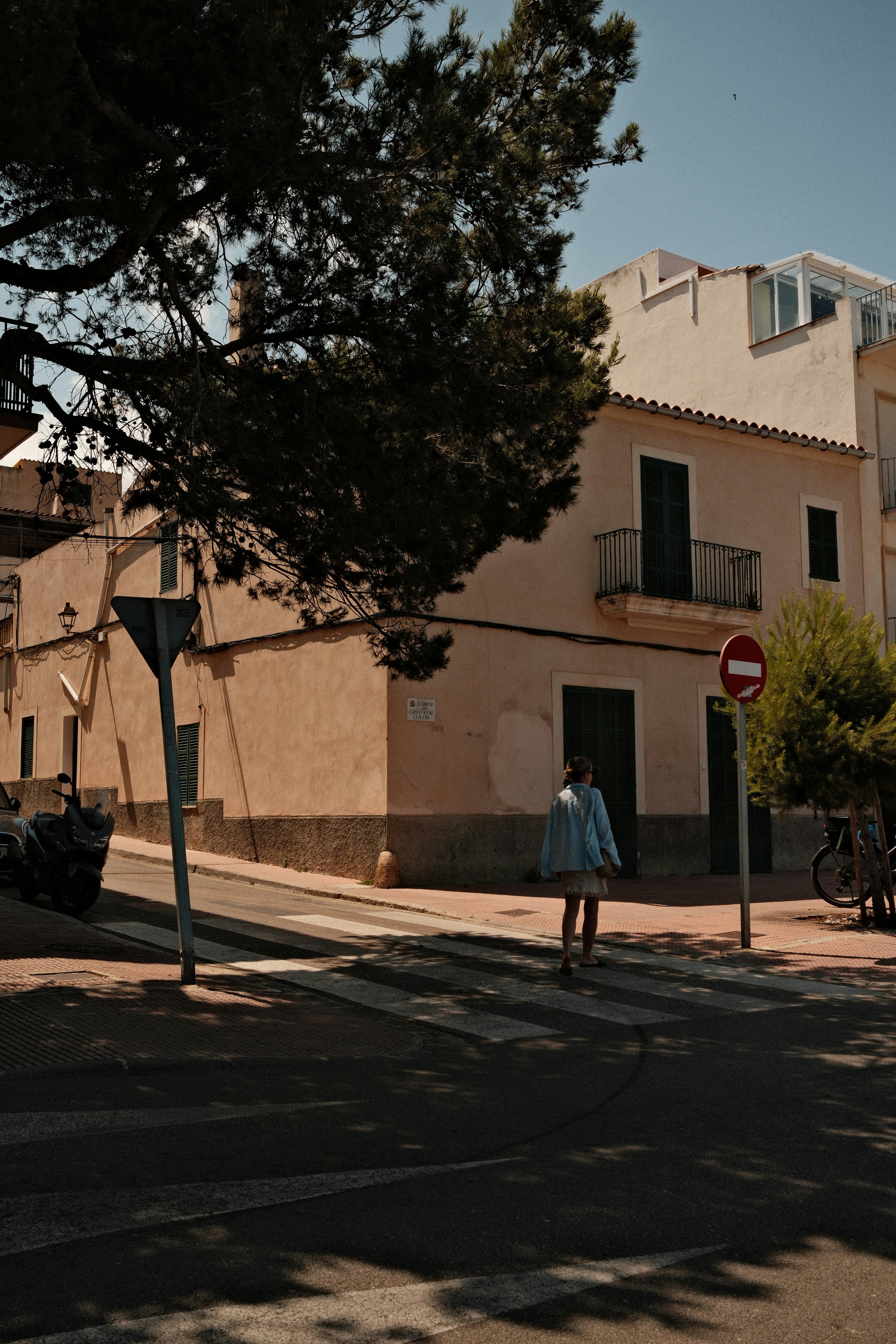 Crossing Shadowed Street: A Woman in Light Blues Near a Peach Building