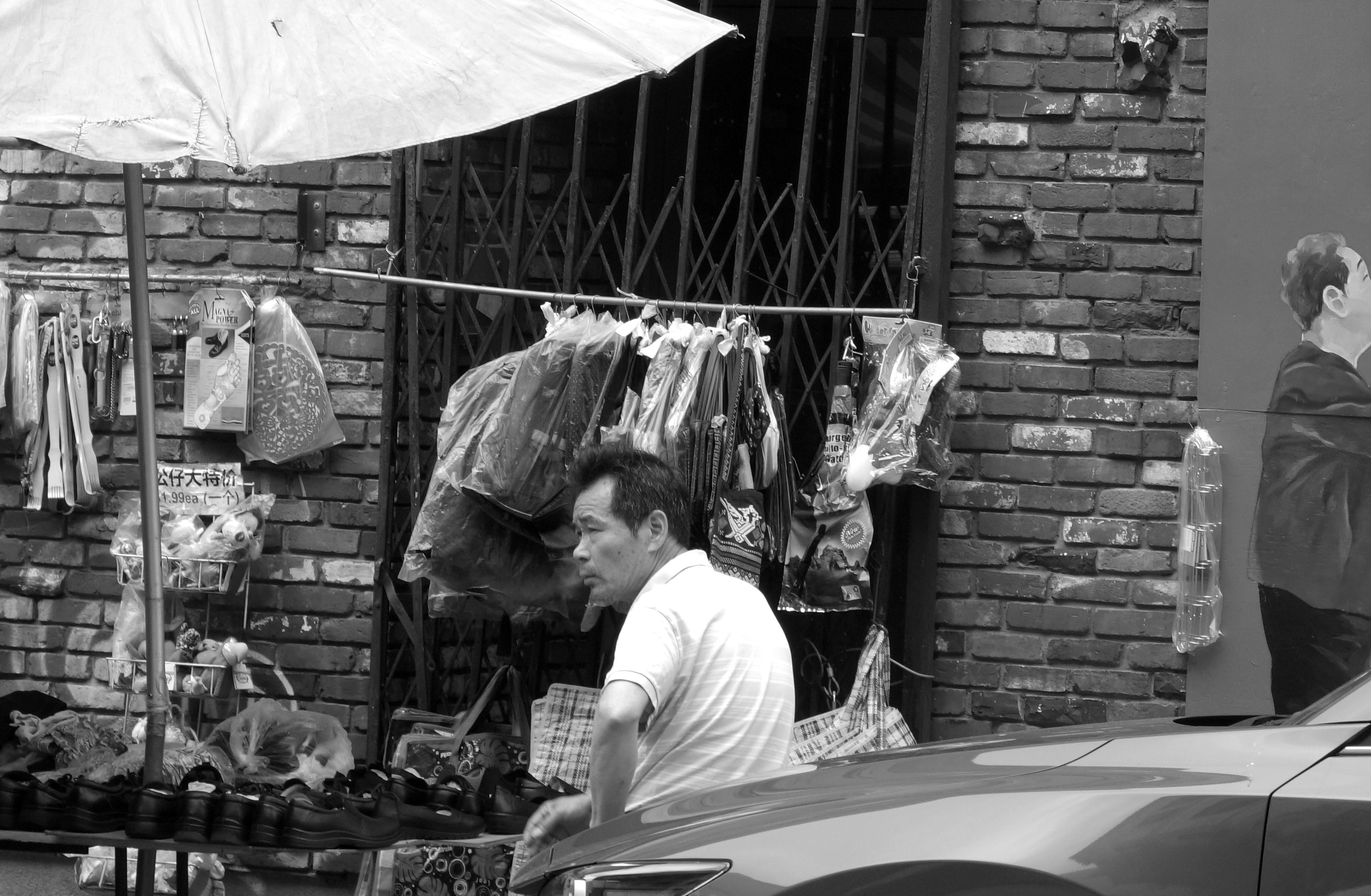 Man in White T-Shirt Atop a City Grocery Stall Echoes Quiet Street Life