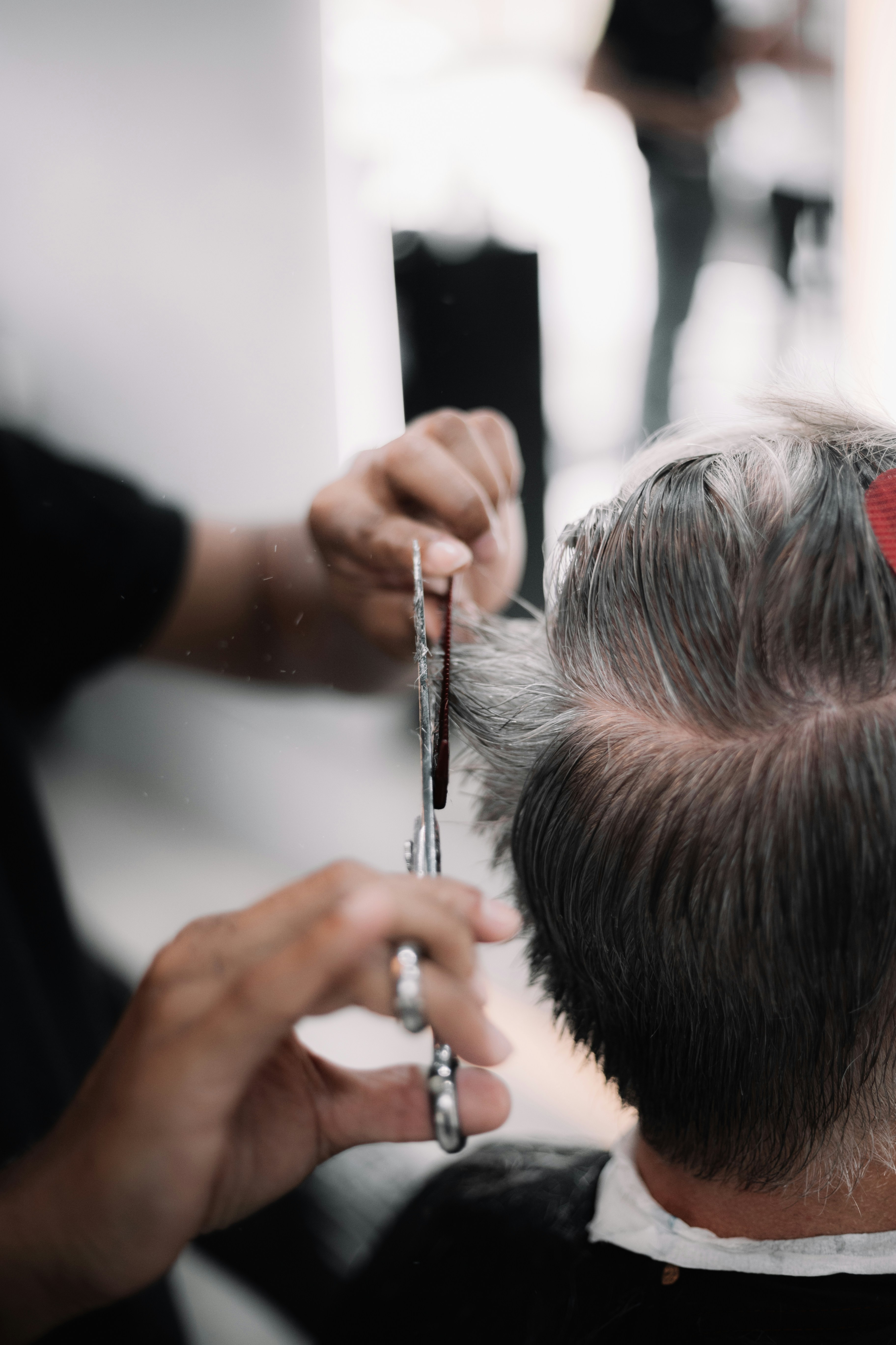 Detalhe de corte de cabelo masculino moderno em salão de beleza ou barbearia profissional. Fotografia em estilo lifestyle capturando a rotina de cuidados masculinos com um corte de cabelo detalhado. O plano detalhe enfatiza a técnica do profissional trabalhando com fios grisalhos/claros sob iluminação natural de estúdio. Ideal para blogs de moda, artigos de bem-estar e materiais de marketing para salões.
