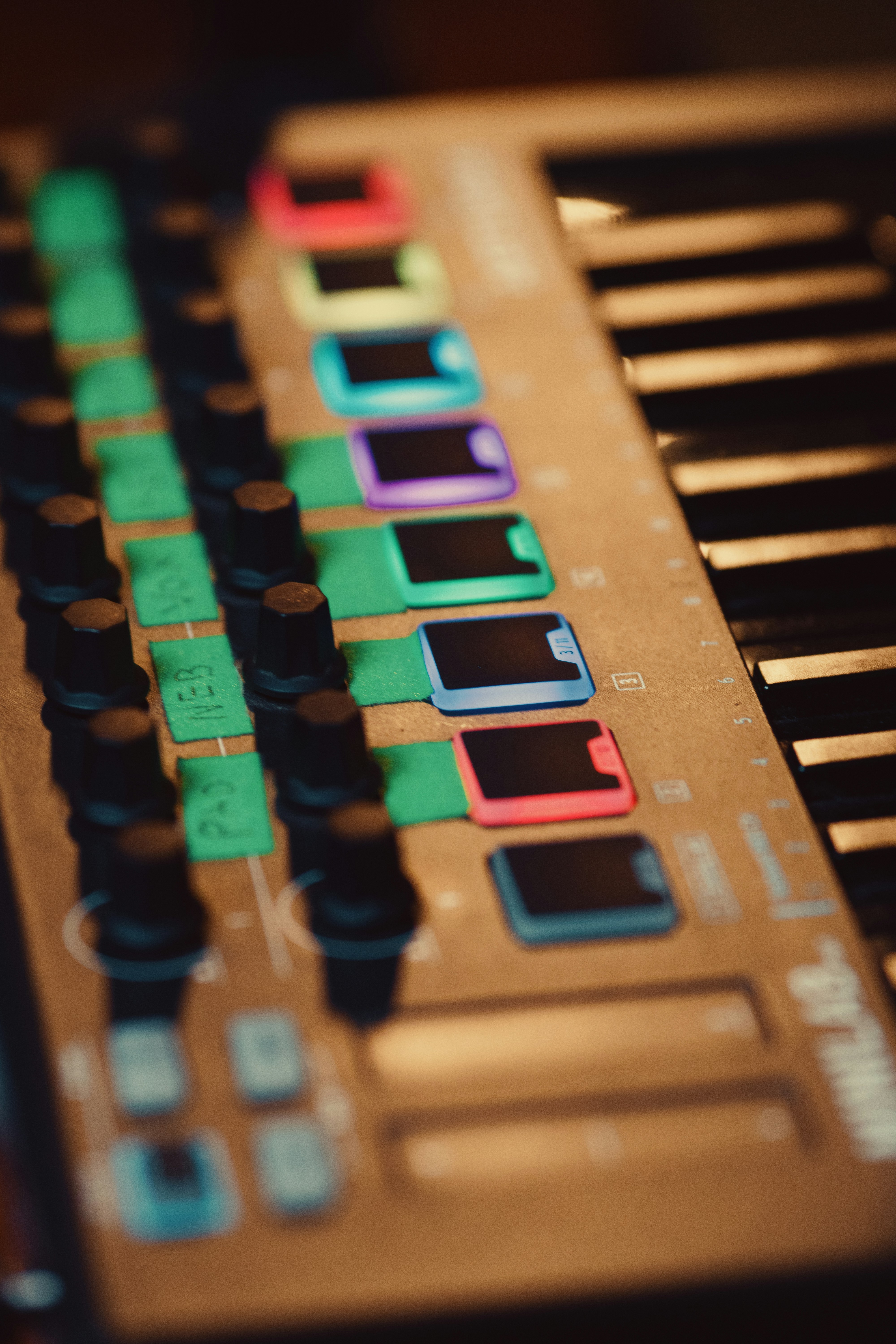 Close-up of a vintage-style audio mixer with multicolored switches and knobs, focusing on the illuminated pads and control surface for emphasis on tactile detail.