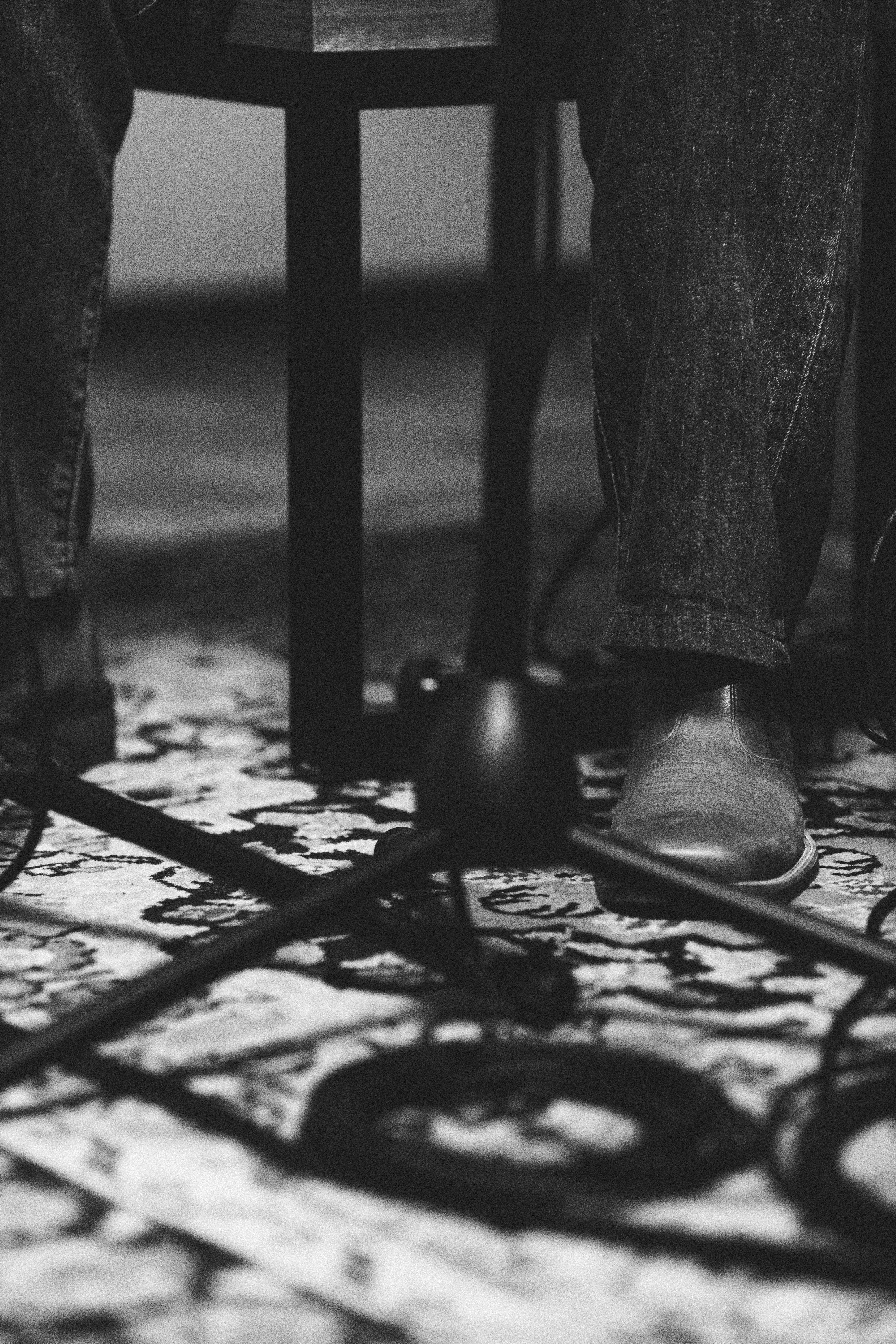Footwear and microphone cable beneath a guitarist's legs on a dark studio rug