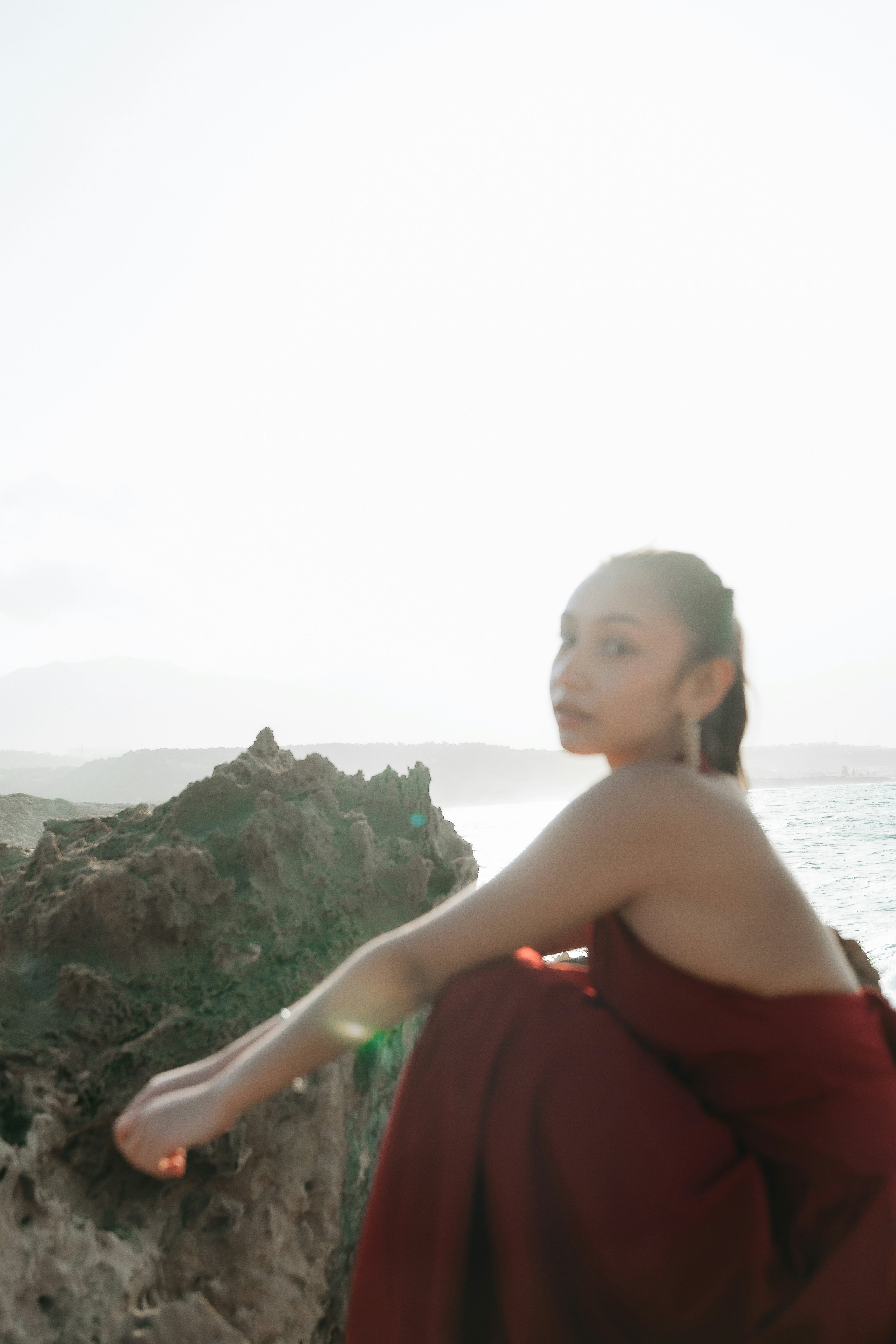Young woman in red dress on rocks by the ocean.