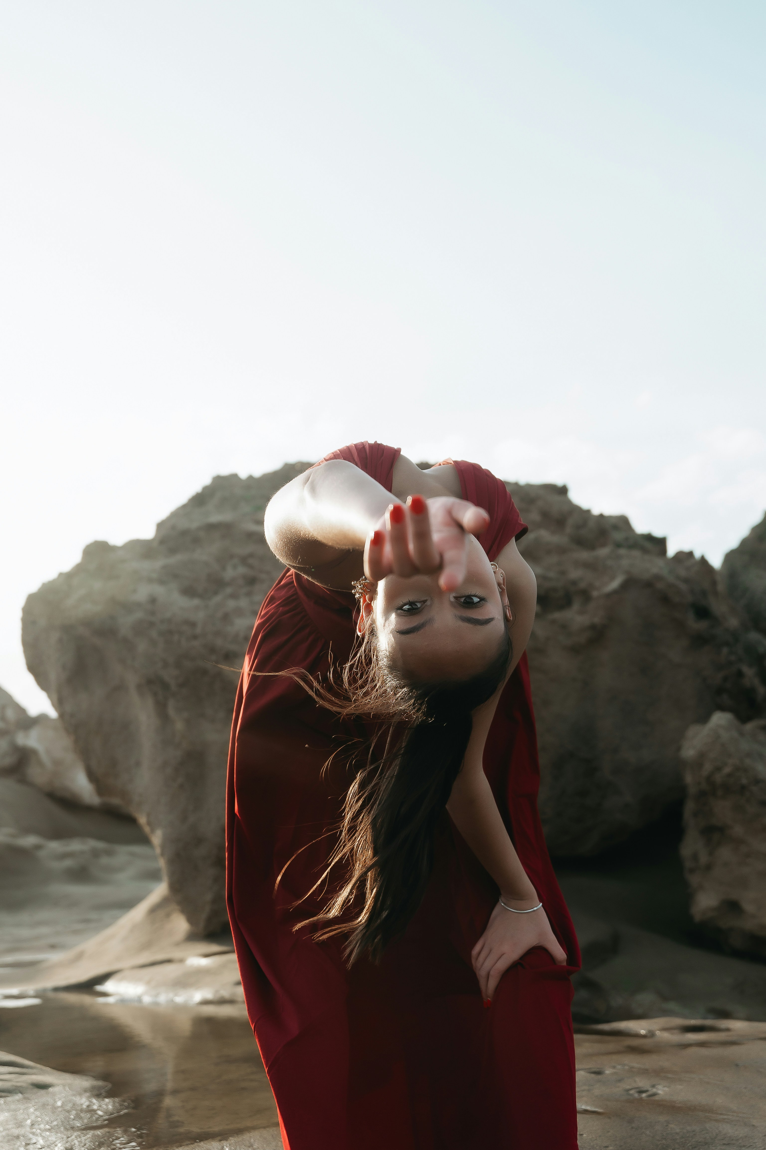 Upside-Down Silhouette: Red Draped Pose Against Coastal Rocks