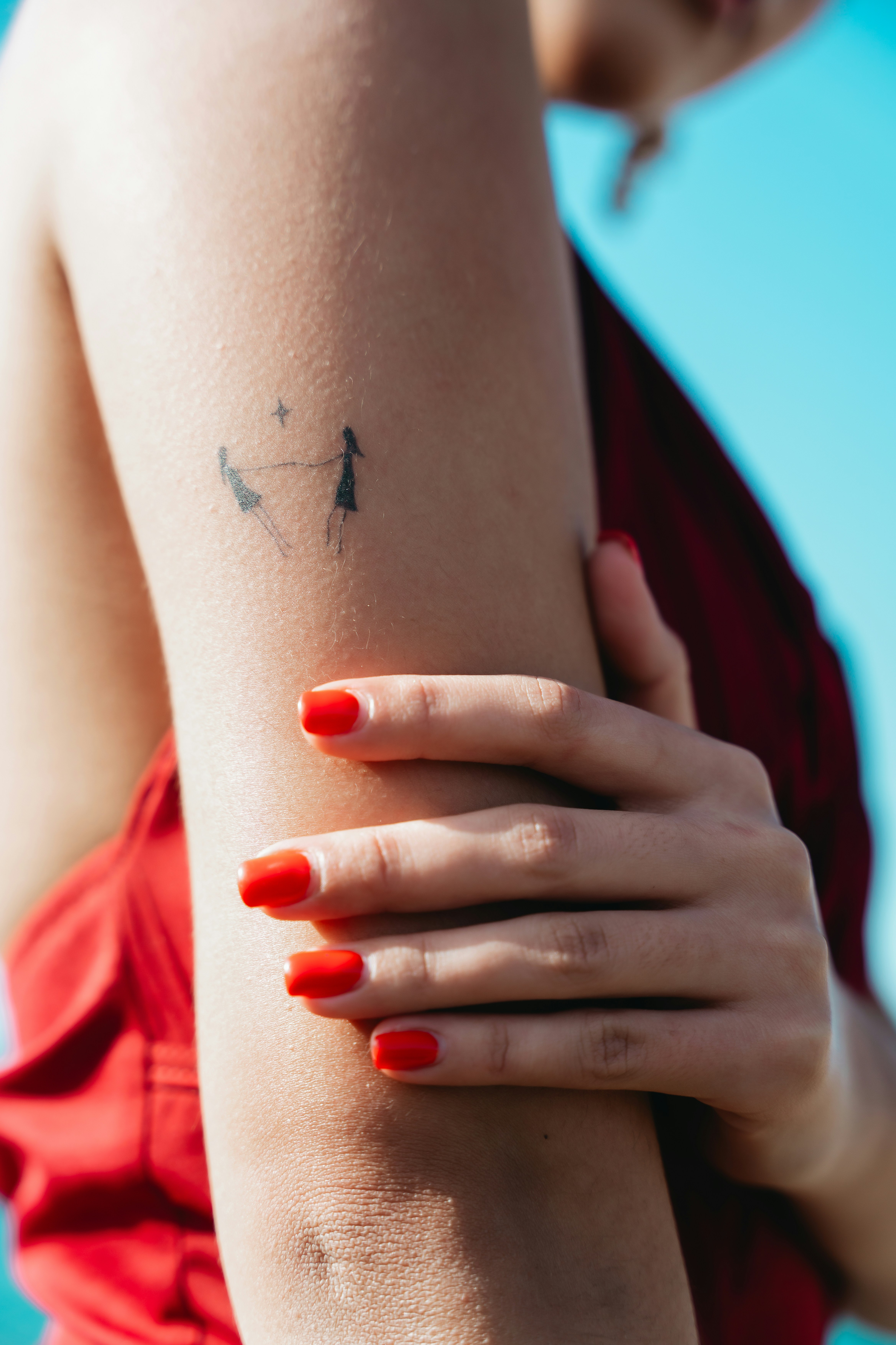 Blue sky, red dress, and a tiny tattoo: a moment of quiet sunlit skin