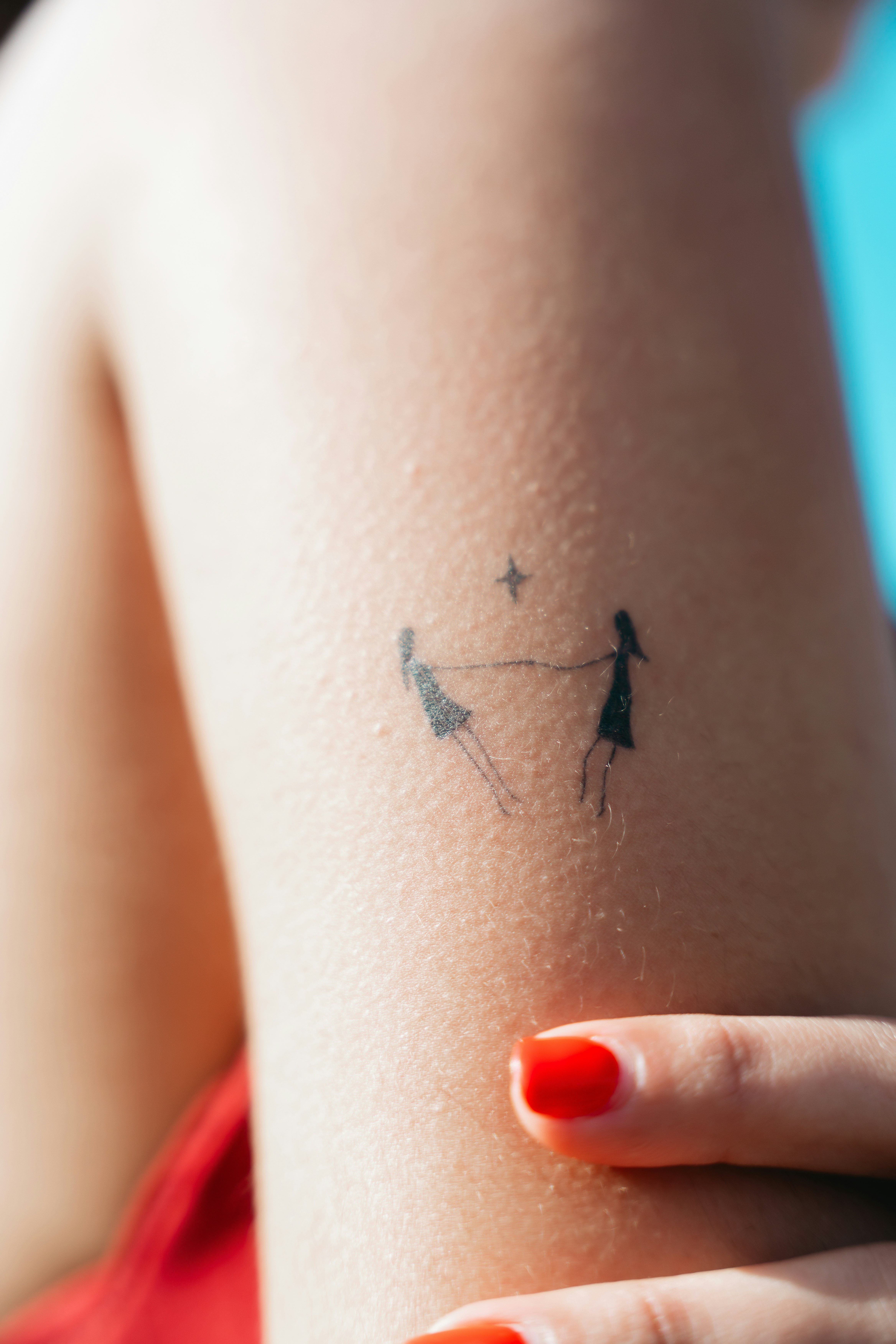 Minimalist tattoo, bold red nail, and sunlit skin in a close-up