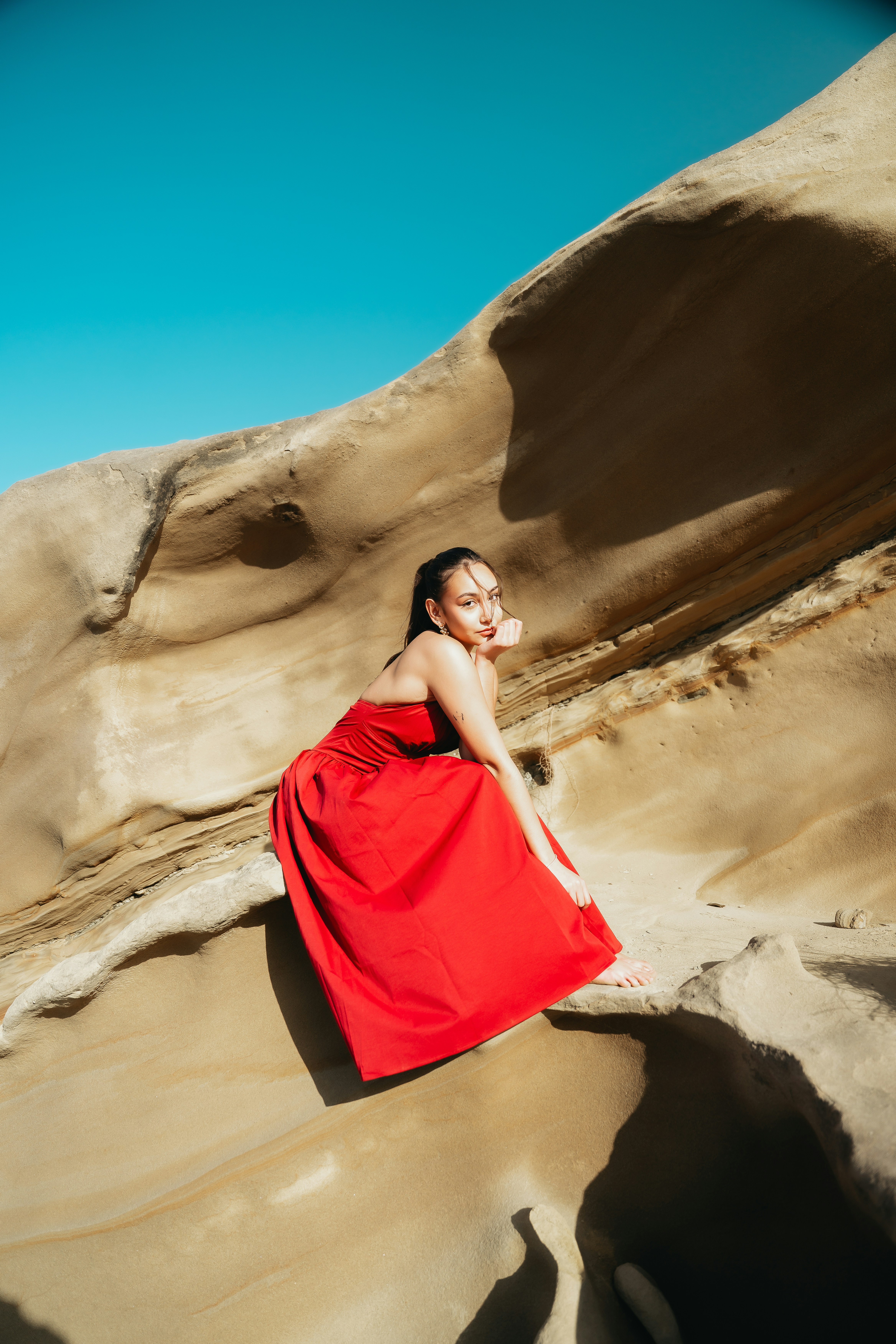 Red Dress, Desert Wall: A Poised Moment on Sunlit Rocks