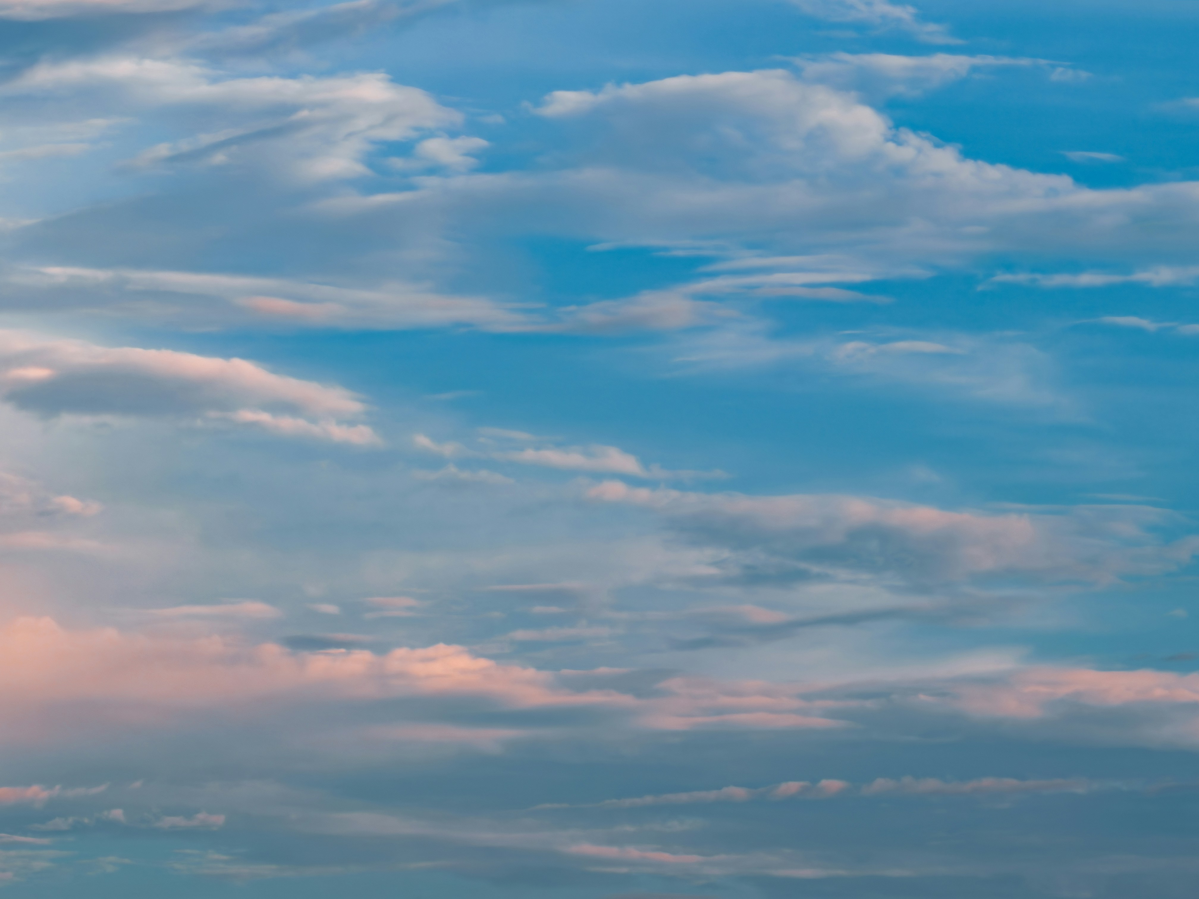 Soft pastel clouds drift across a calm blue sky, creating a serene, expansive horizon without a defined foreground subject. This image emphasizes atmosphere and color gradients.