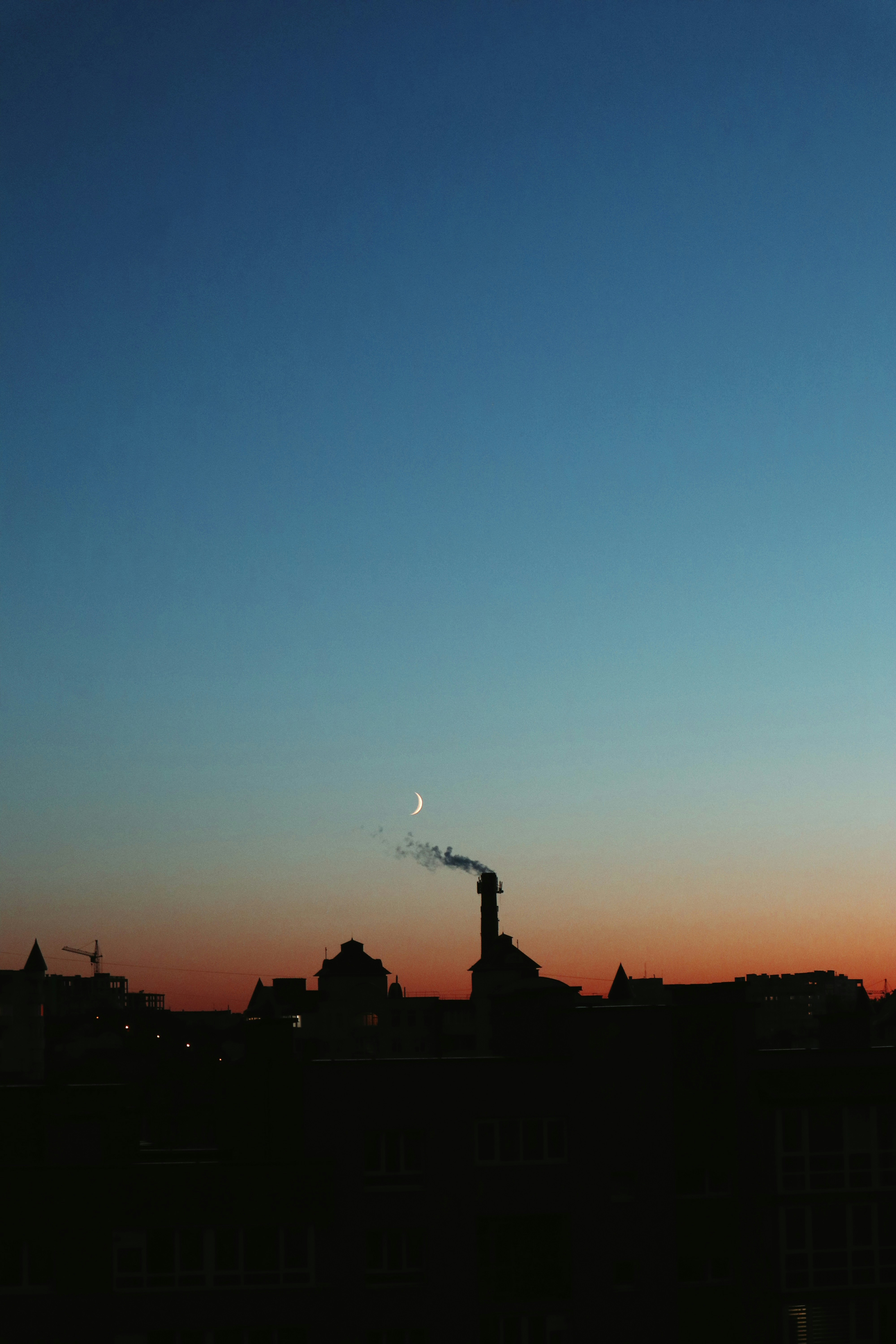 City skyline of Ternopil at night. Crescent moon and silhouette of chimney in twilight sky.