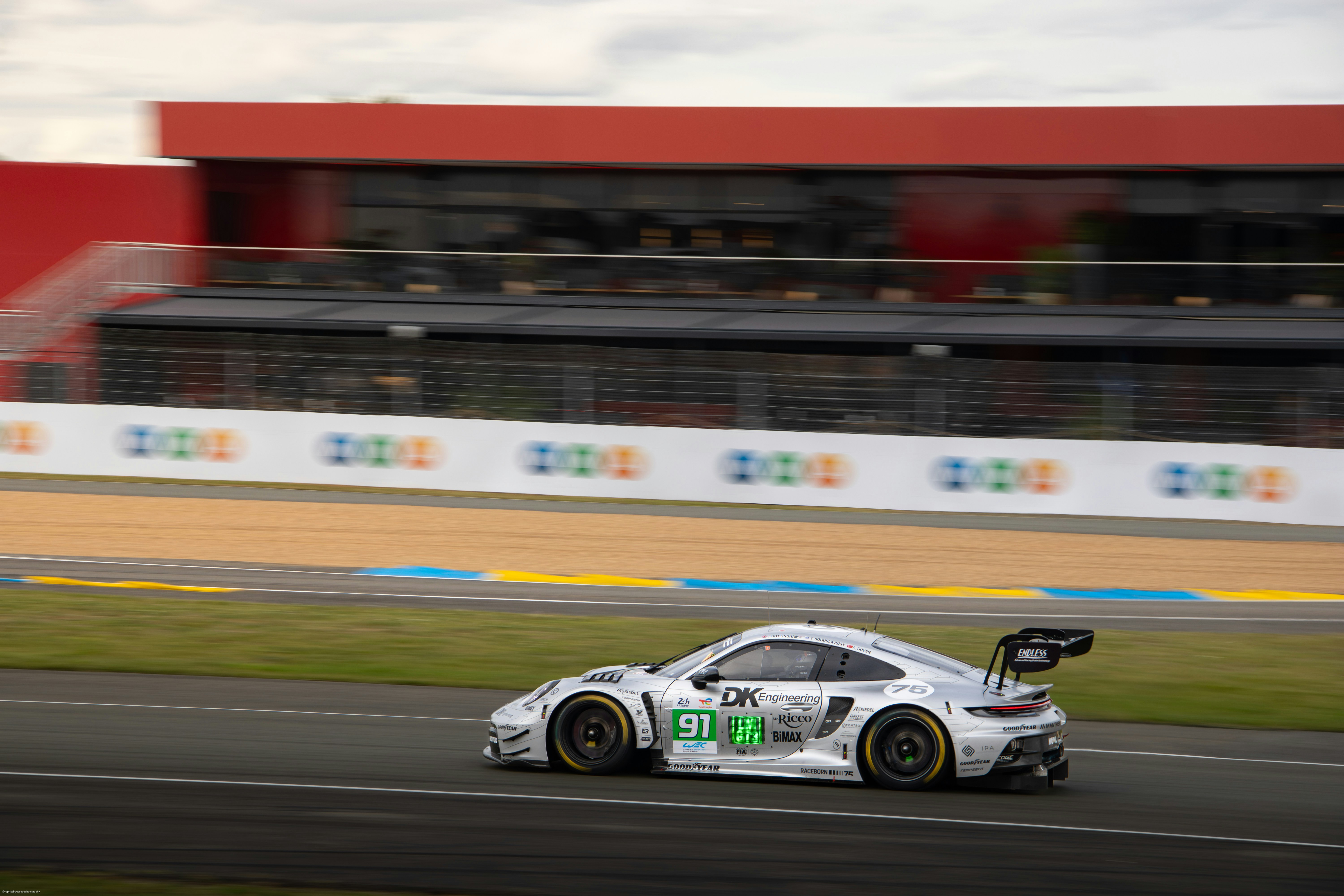 Silver racing car leans into a high-speed sprint on a sunlit circuit