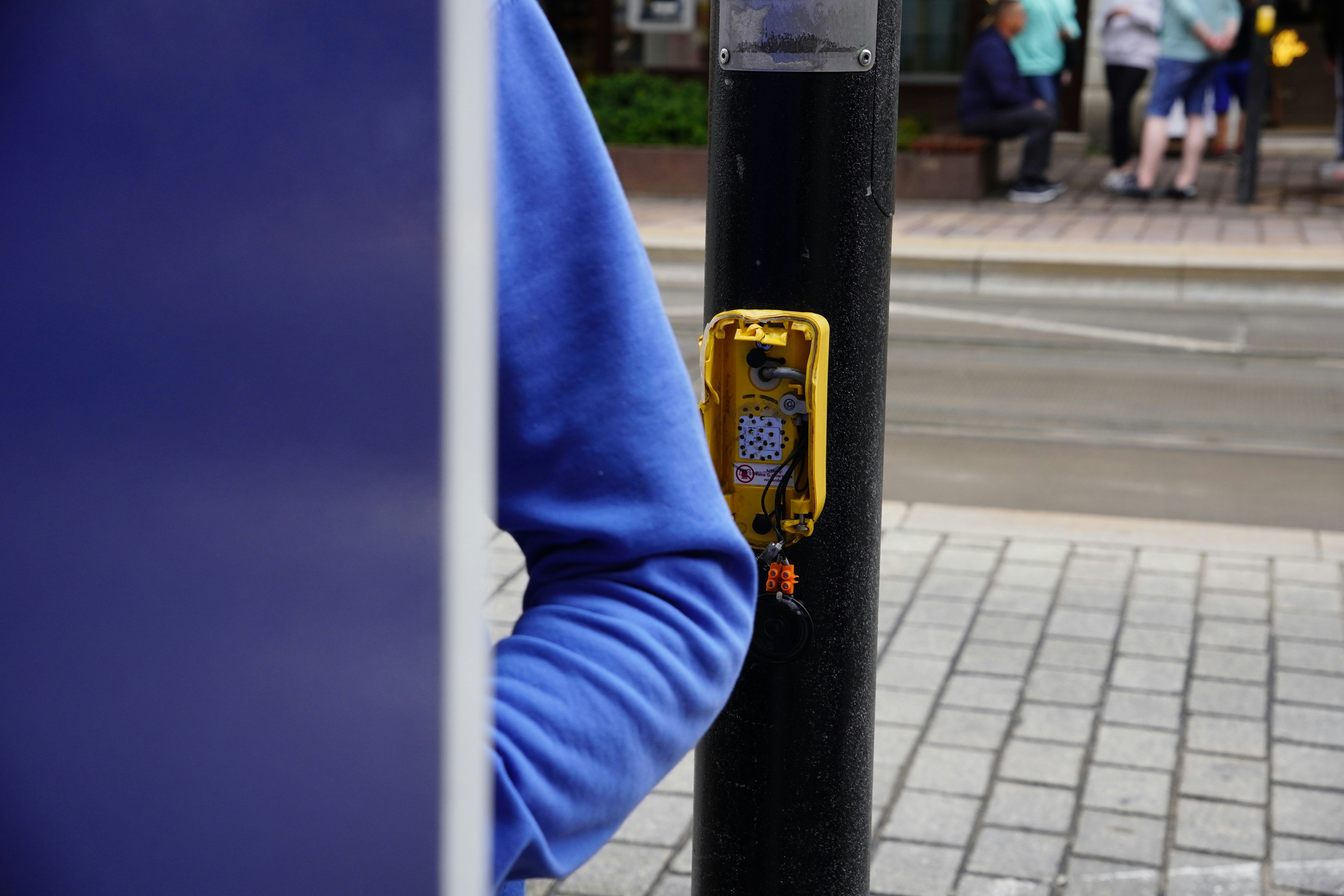 Blue-sleeved person near a damaged pedestrian crossing button.
