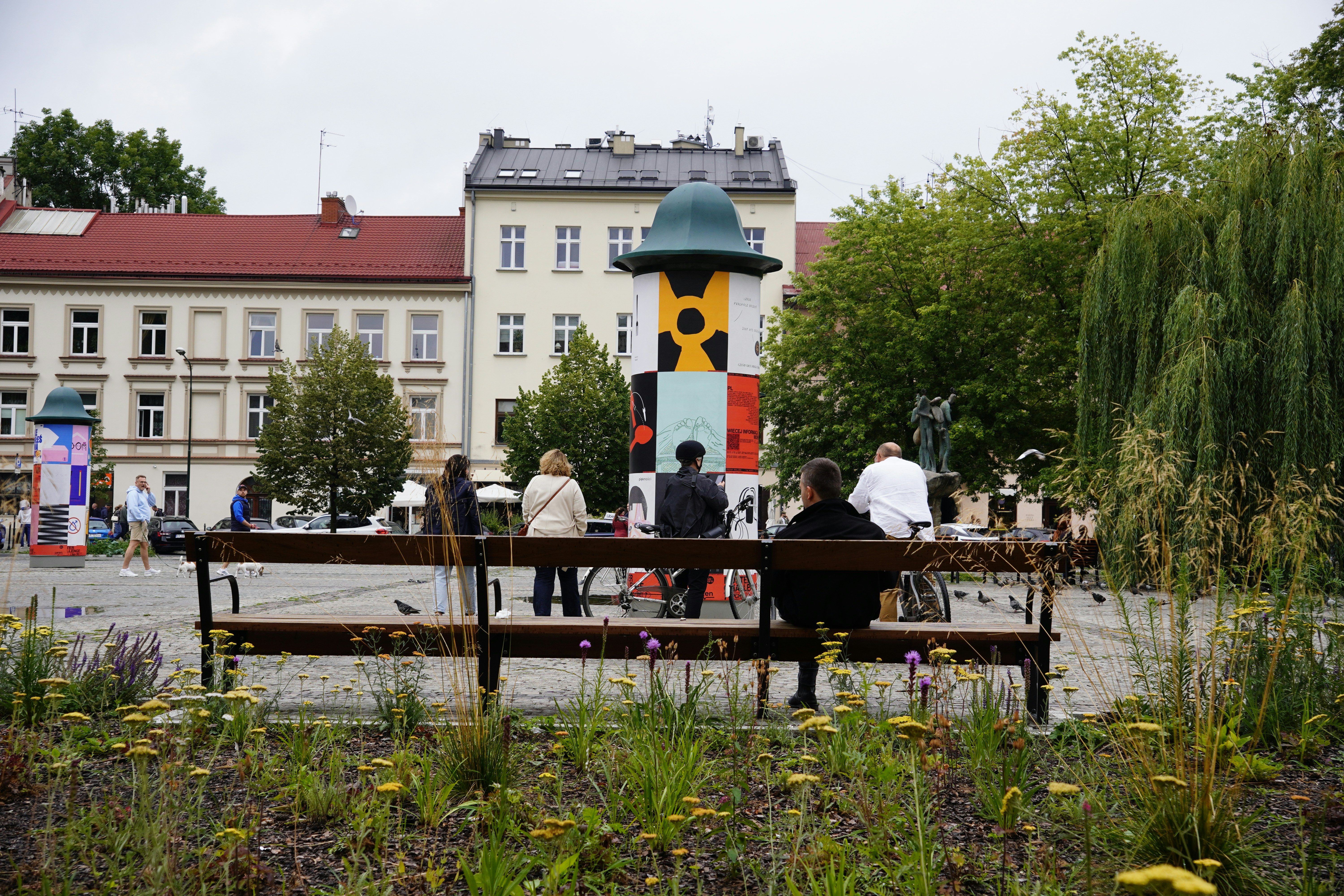 Colorful sculpture and people on a park bench in front of a row of pastel buildings