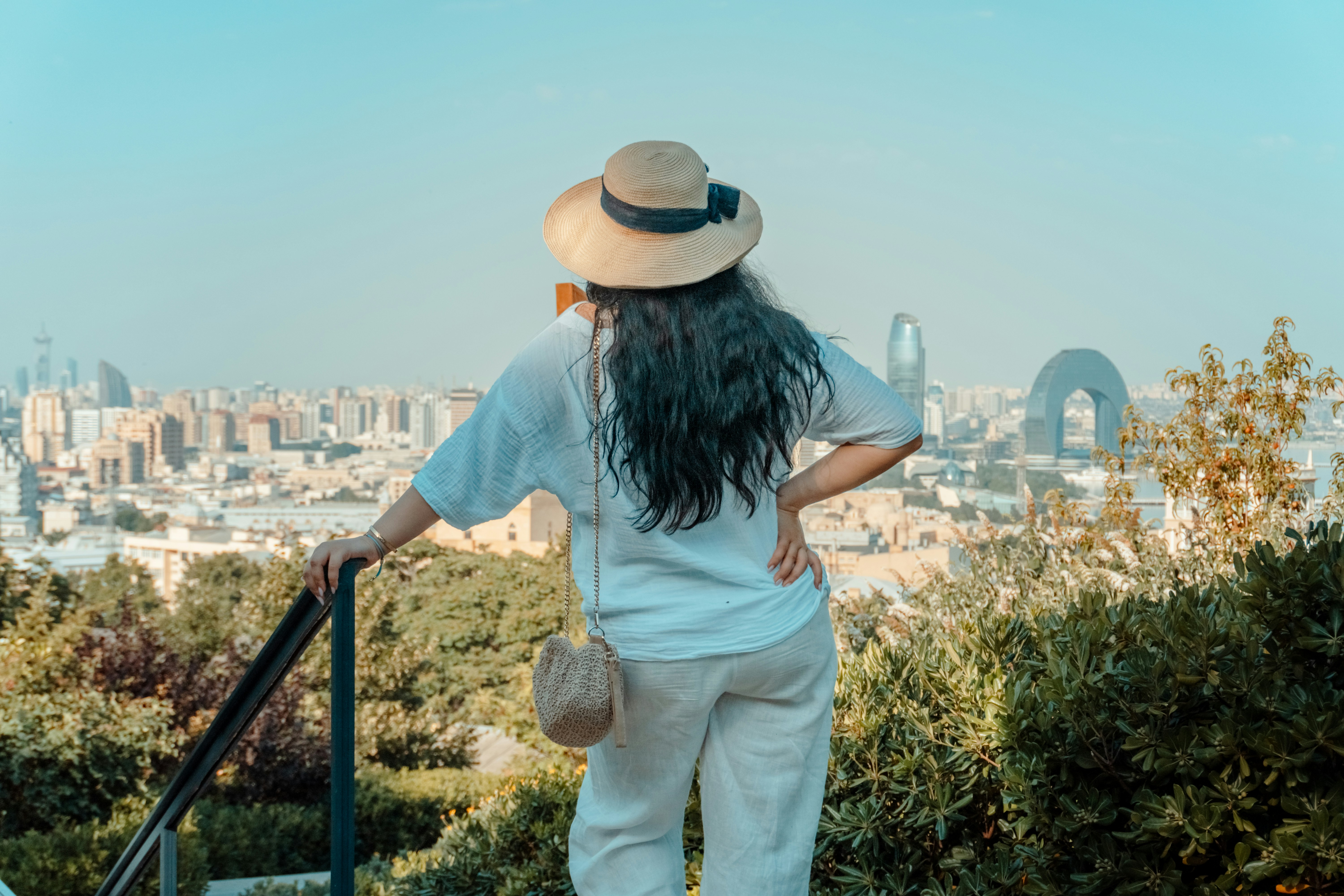 Traveler on a Hillside Overlook: Cityscape Unfolding Beyond a Hat-Wedged View