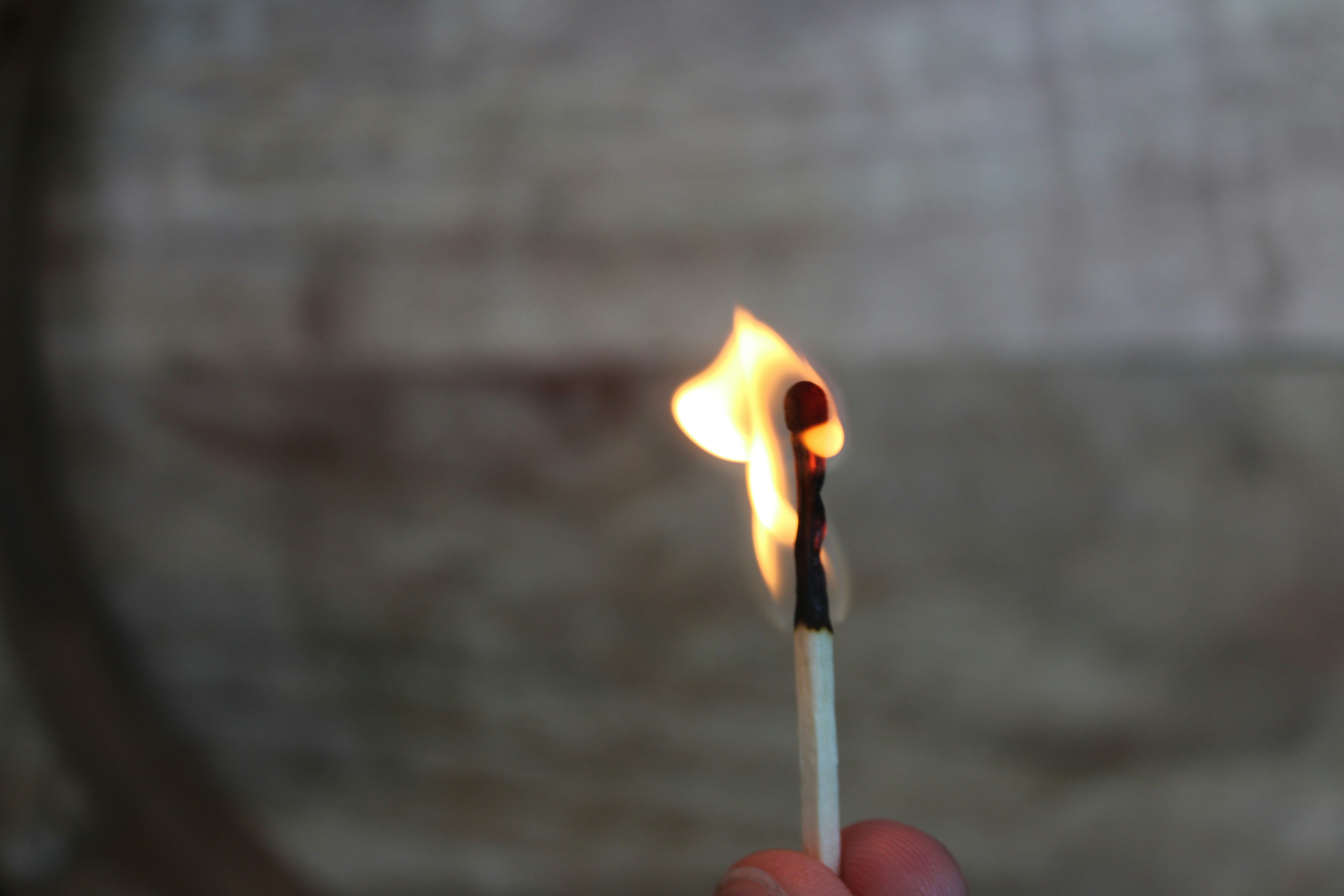 A solitary match awakens a small flame against a blurred wooden backdrop