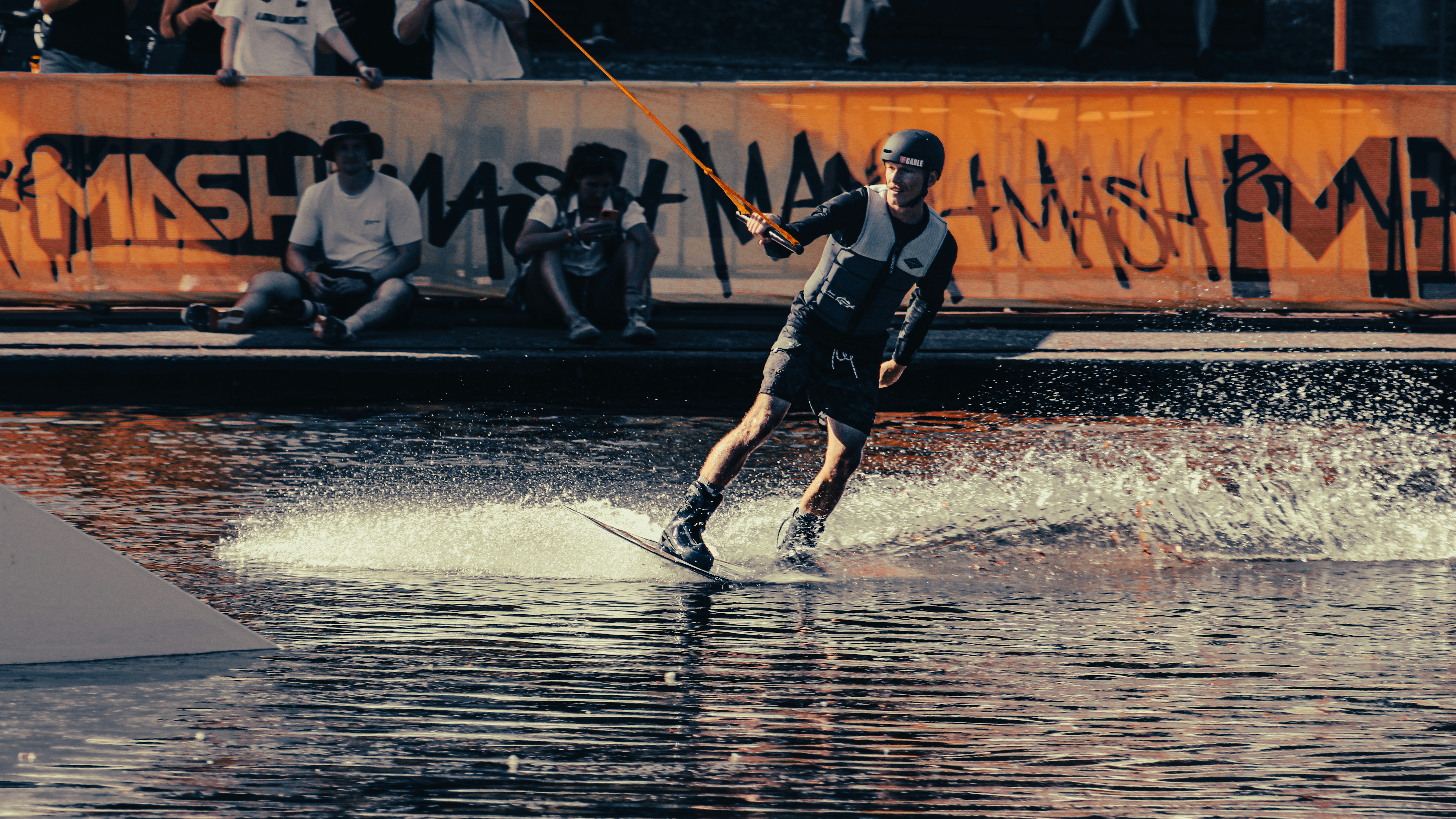 Toward the Wake: A Skateboarder Glides Across Shimmering Water Under Arena Barriers